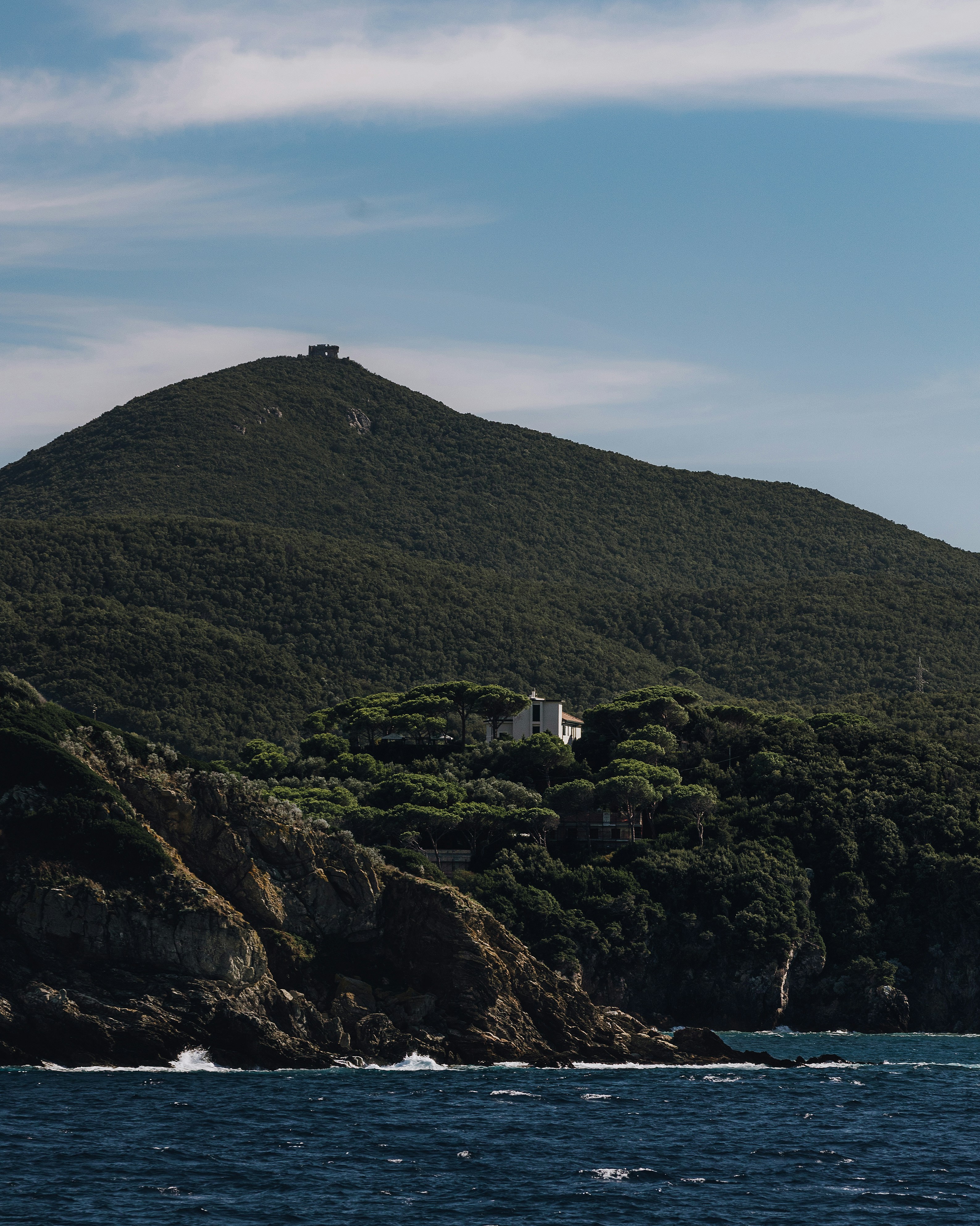 White building nestled on a green hillside overlooking the ocean