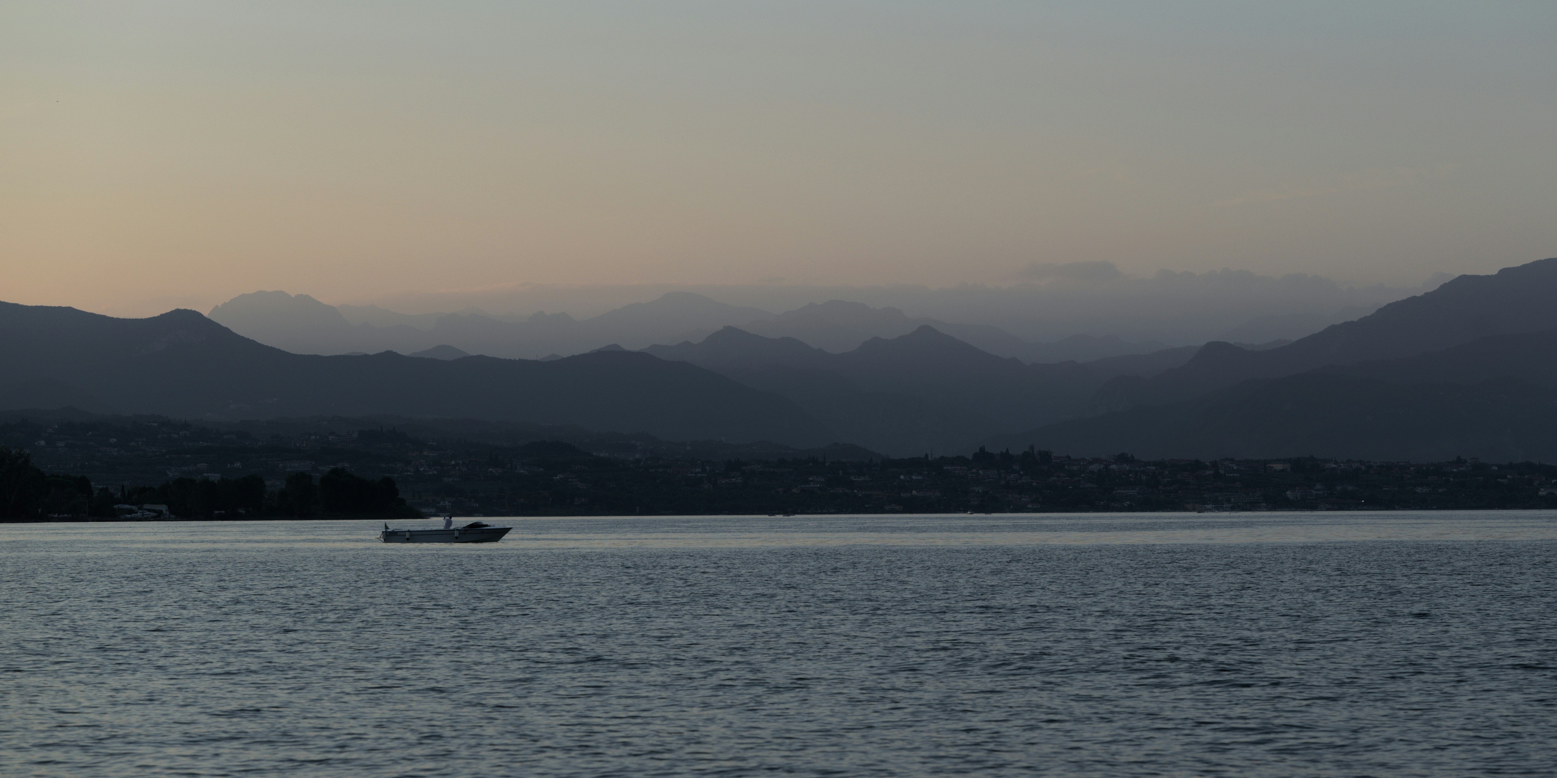 A lone boat sails on a calm lake at dusk.