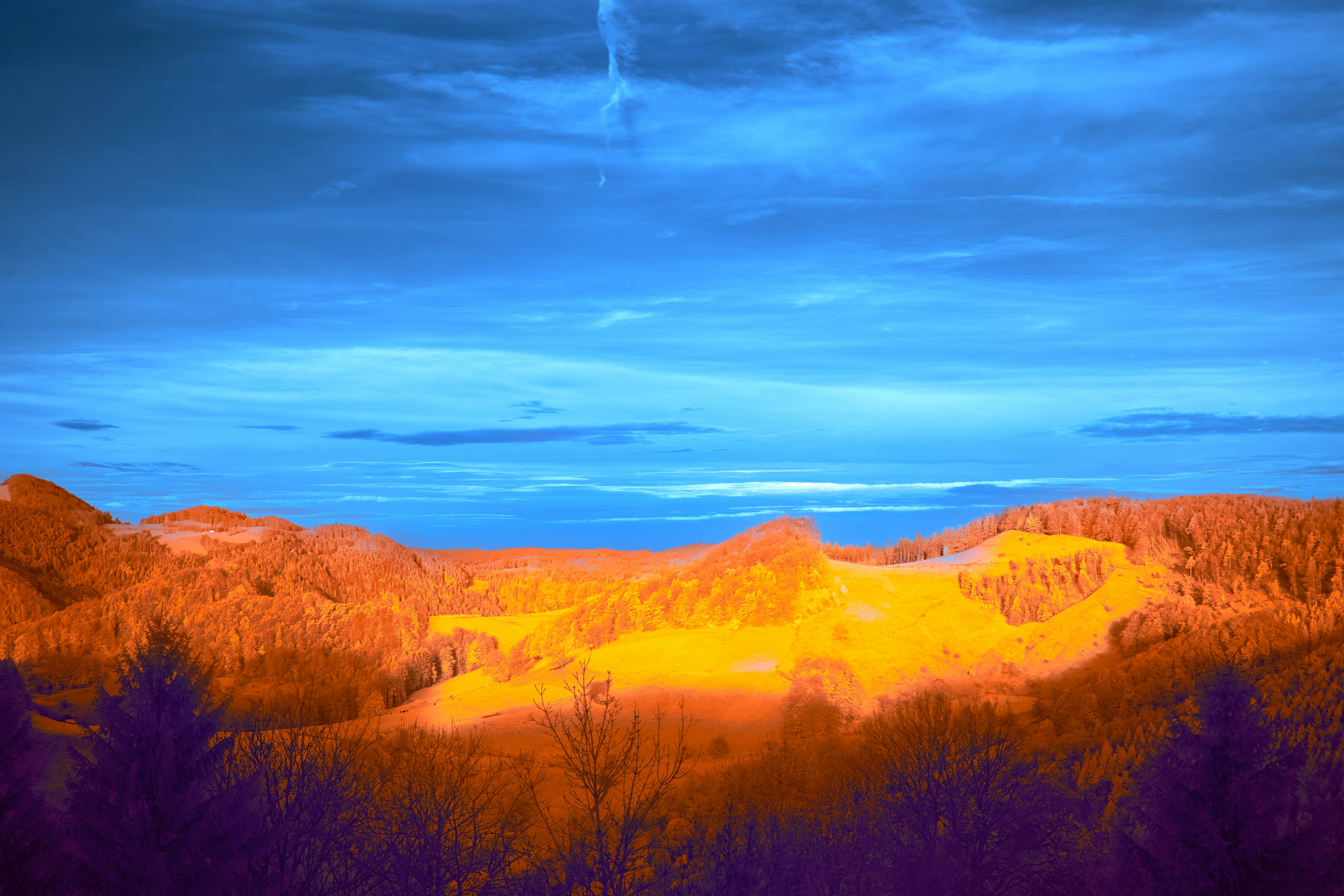 Vividly colored hills bathed in orange and purple hues under a dynamic sky, showcasing a surreal interpretation of a natural landscape.