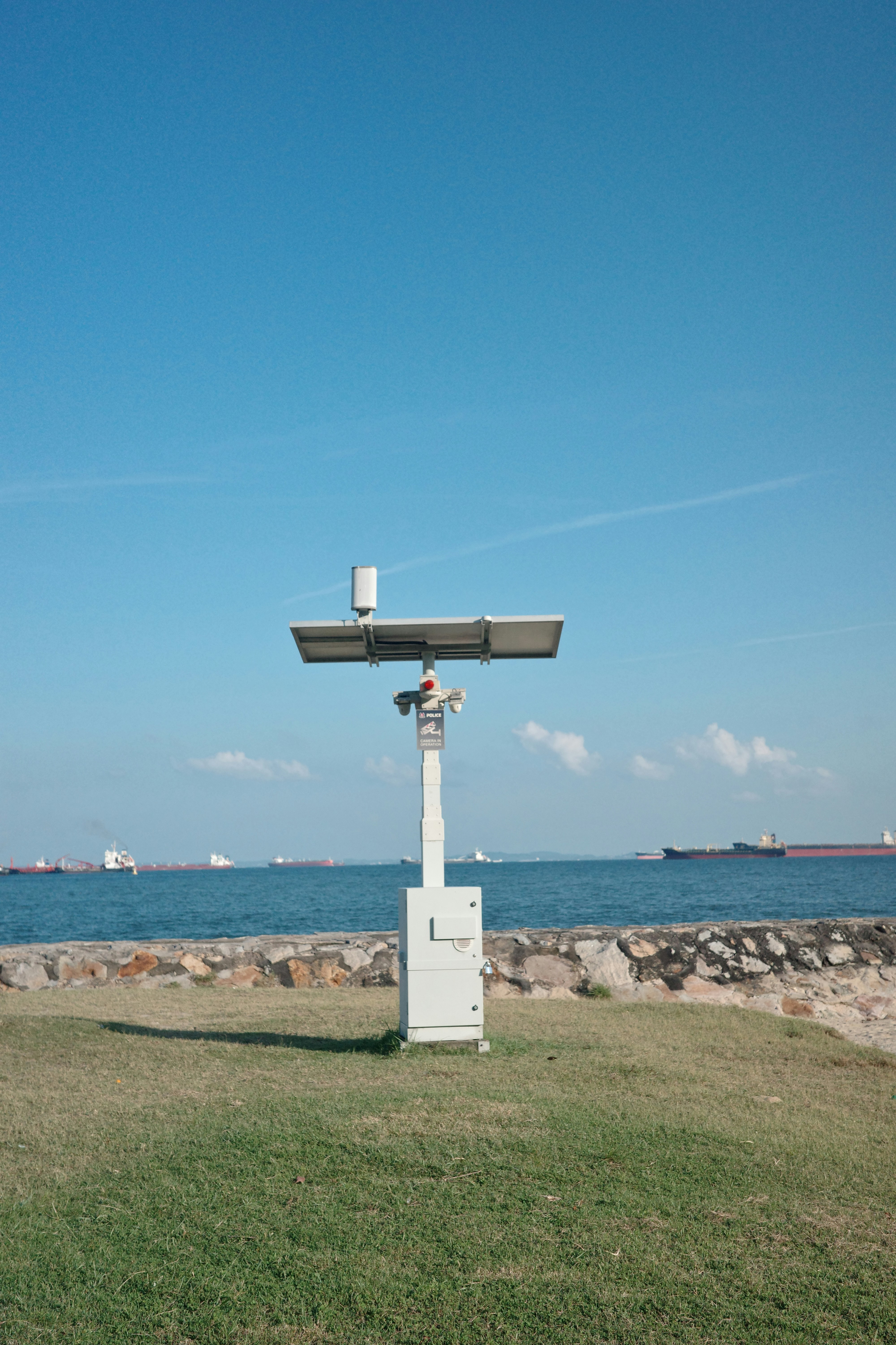 Solar powered weather station on grassy area by the sea.