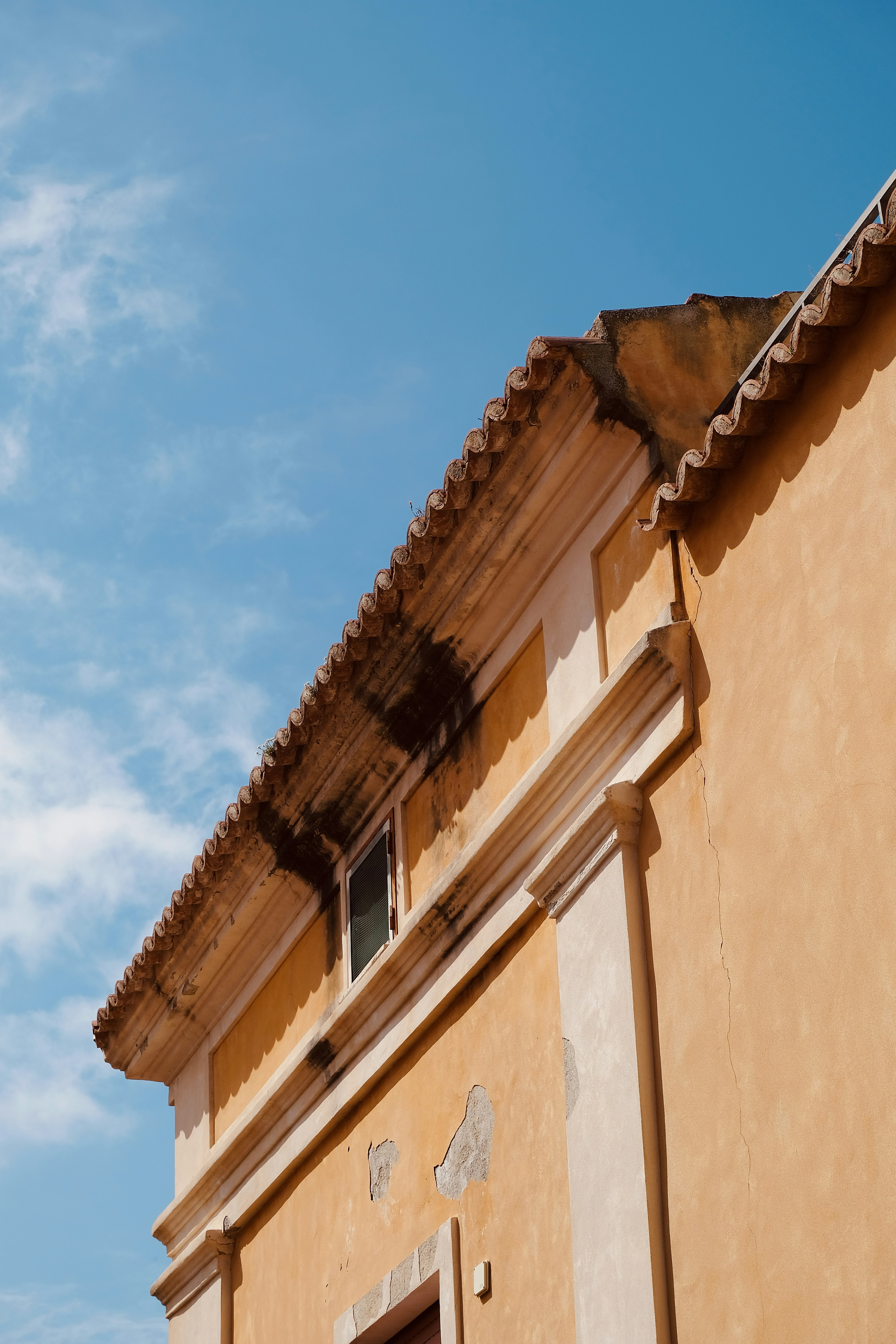 Historic building corner showcasing weathered textures and architectural details against a vibrant blue sky.