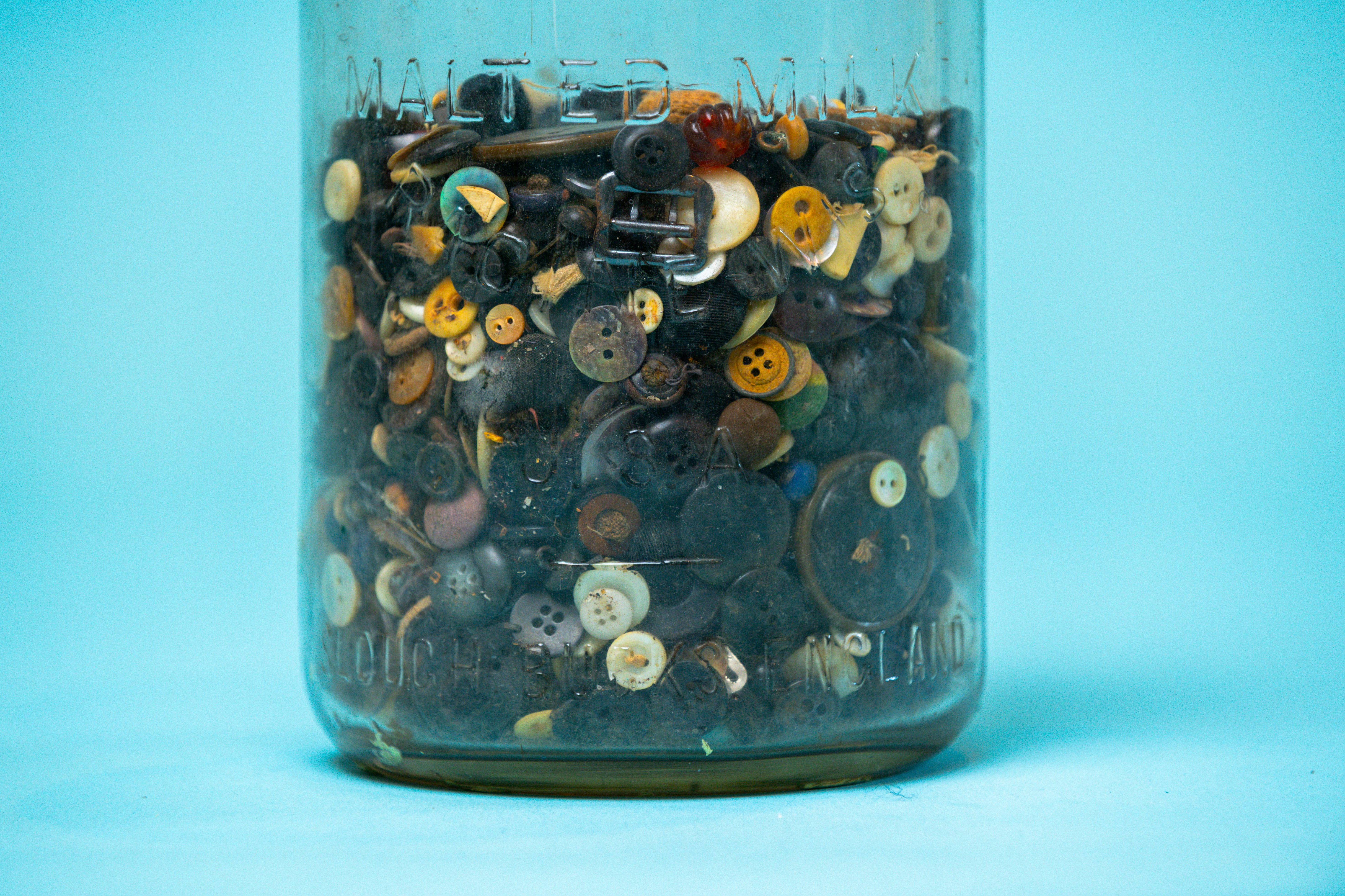 Glass jar filled with assorted buttons on blue background