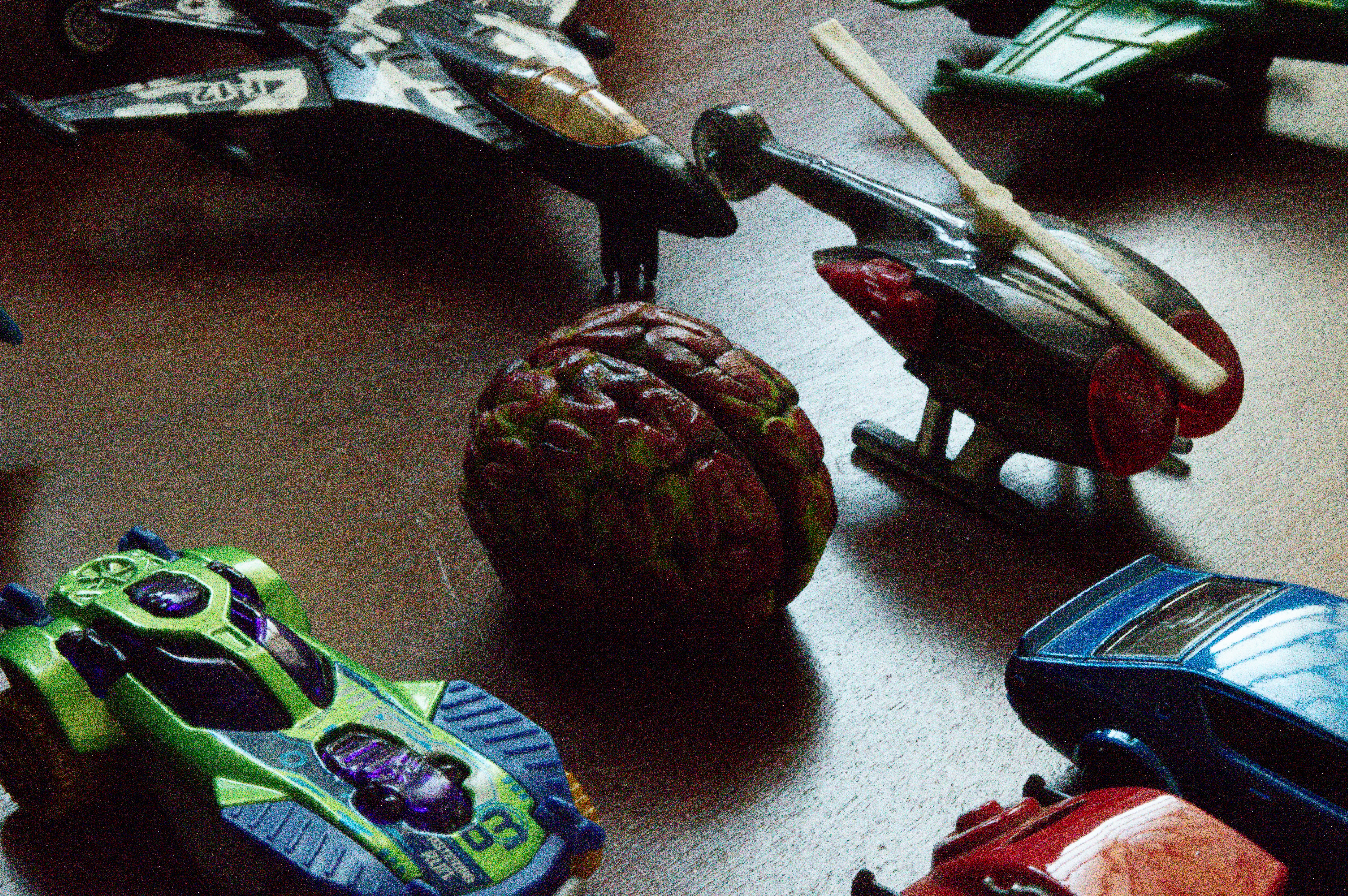 A colorful array of toy vehicles and a unique brain-shaped toy arranged on a wooden surface.