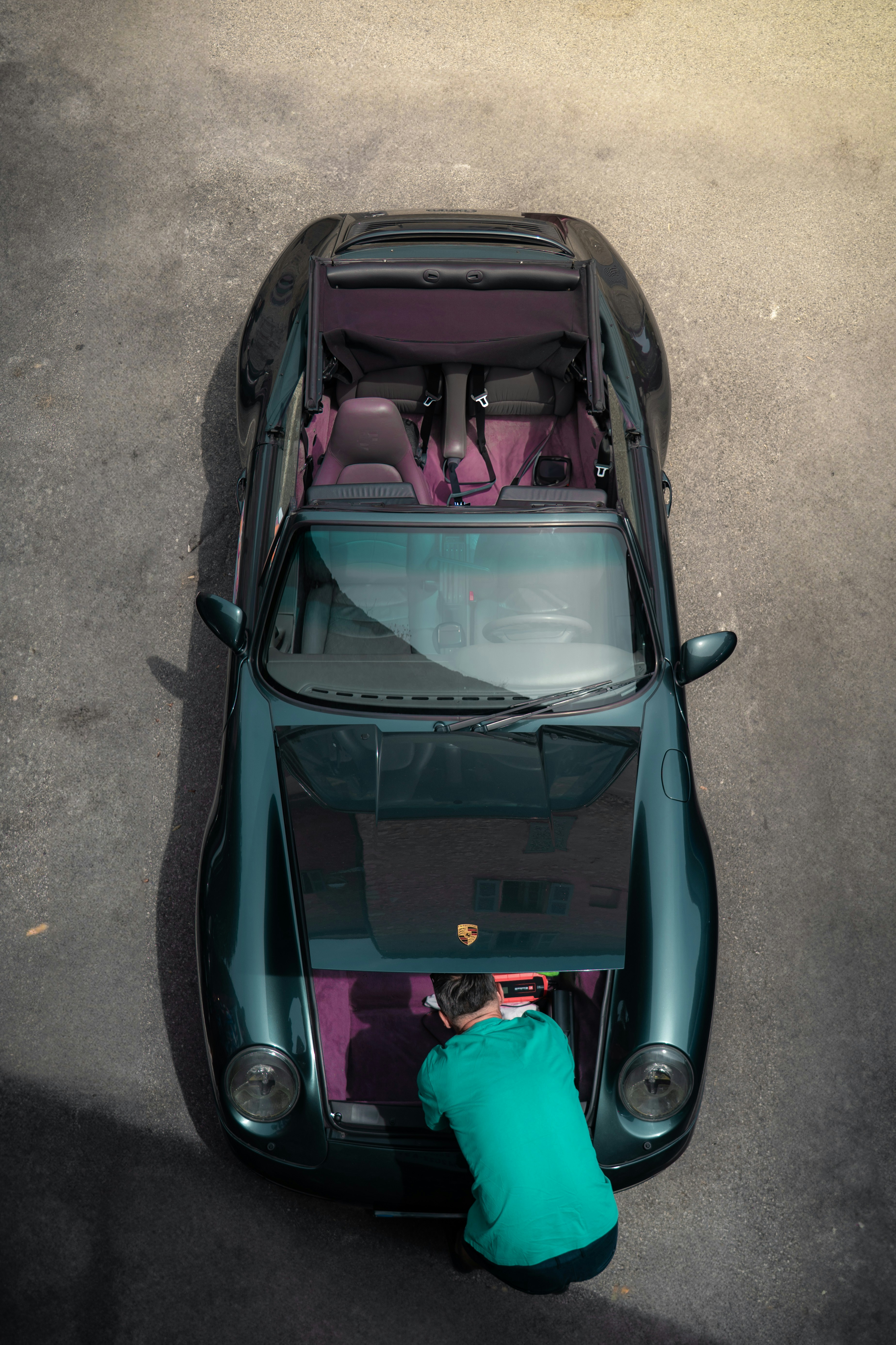 A mechanic inspects the engine compartment of a vintage Porsche convertible, showcasing the car's unique interior and design elements.