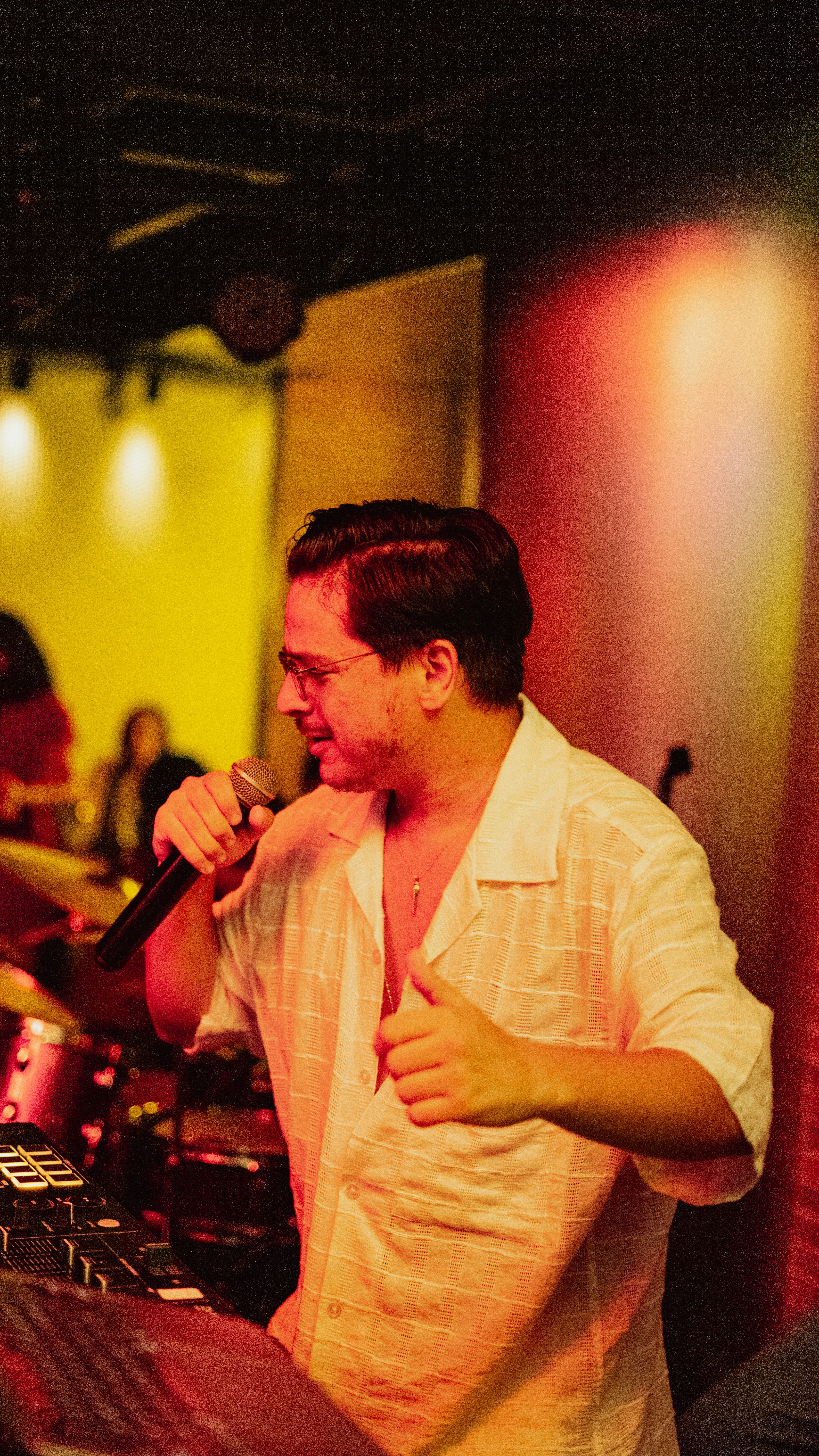 A performer passionately engages with the audience while singing into a microphone, surrounded by musical instruments and warm lighting.