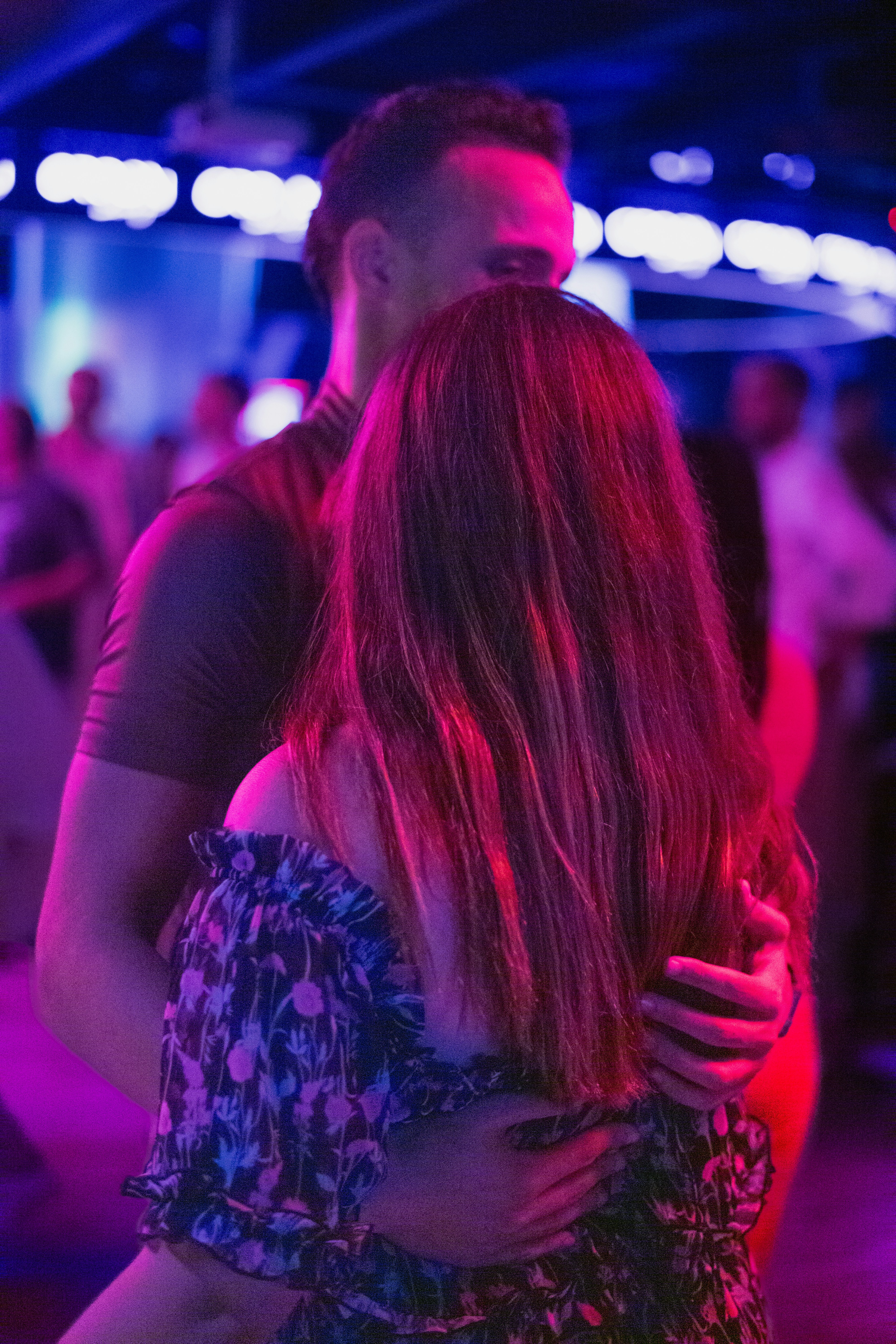 Couple dancing closely in a vibrant, illuminated setting, with colorful lighting enhancing the intimate moment.