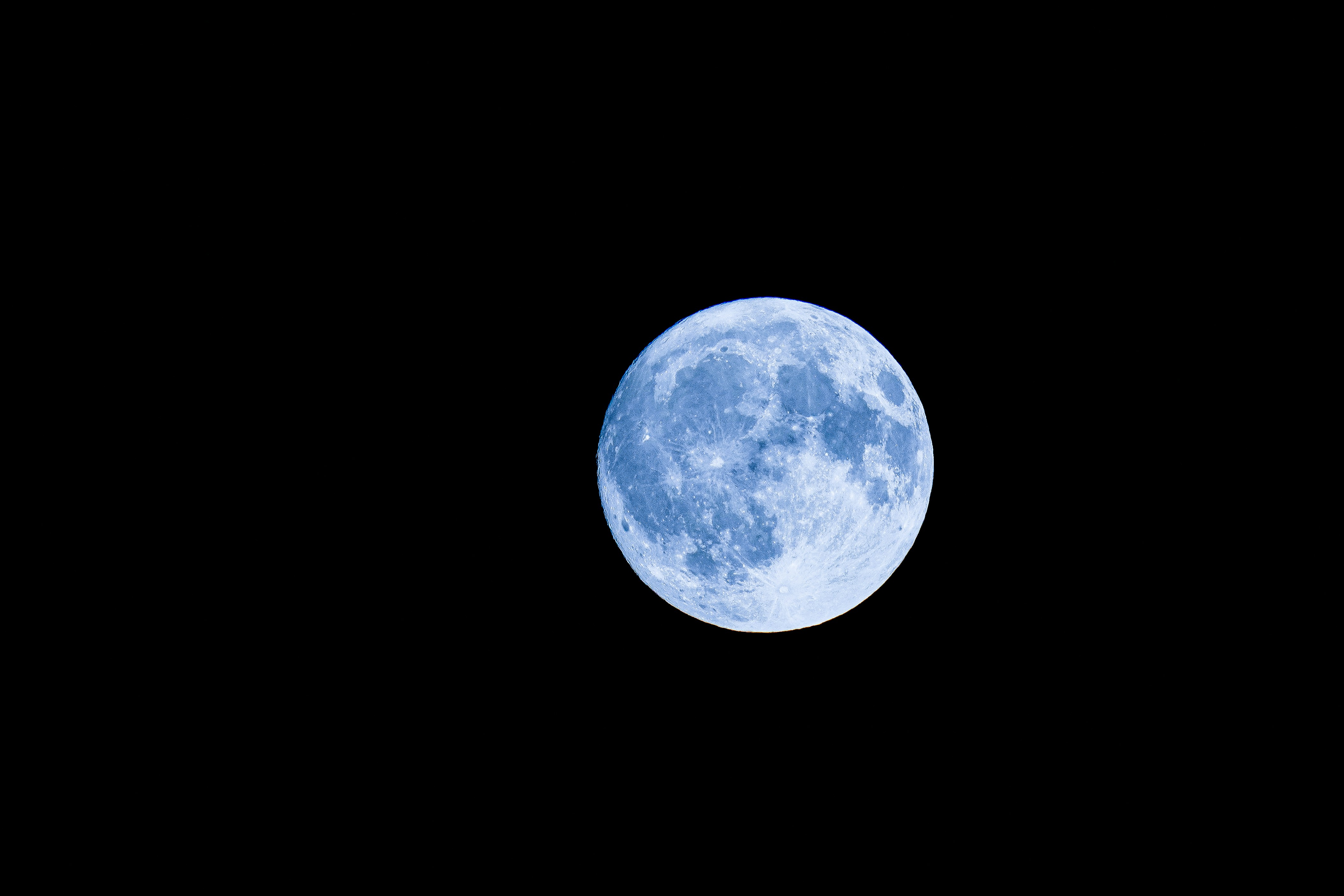 A bright blue moon shines in the dark night sky.
