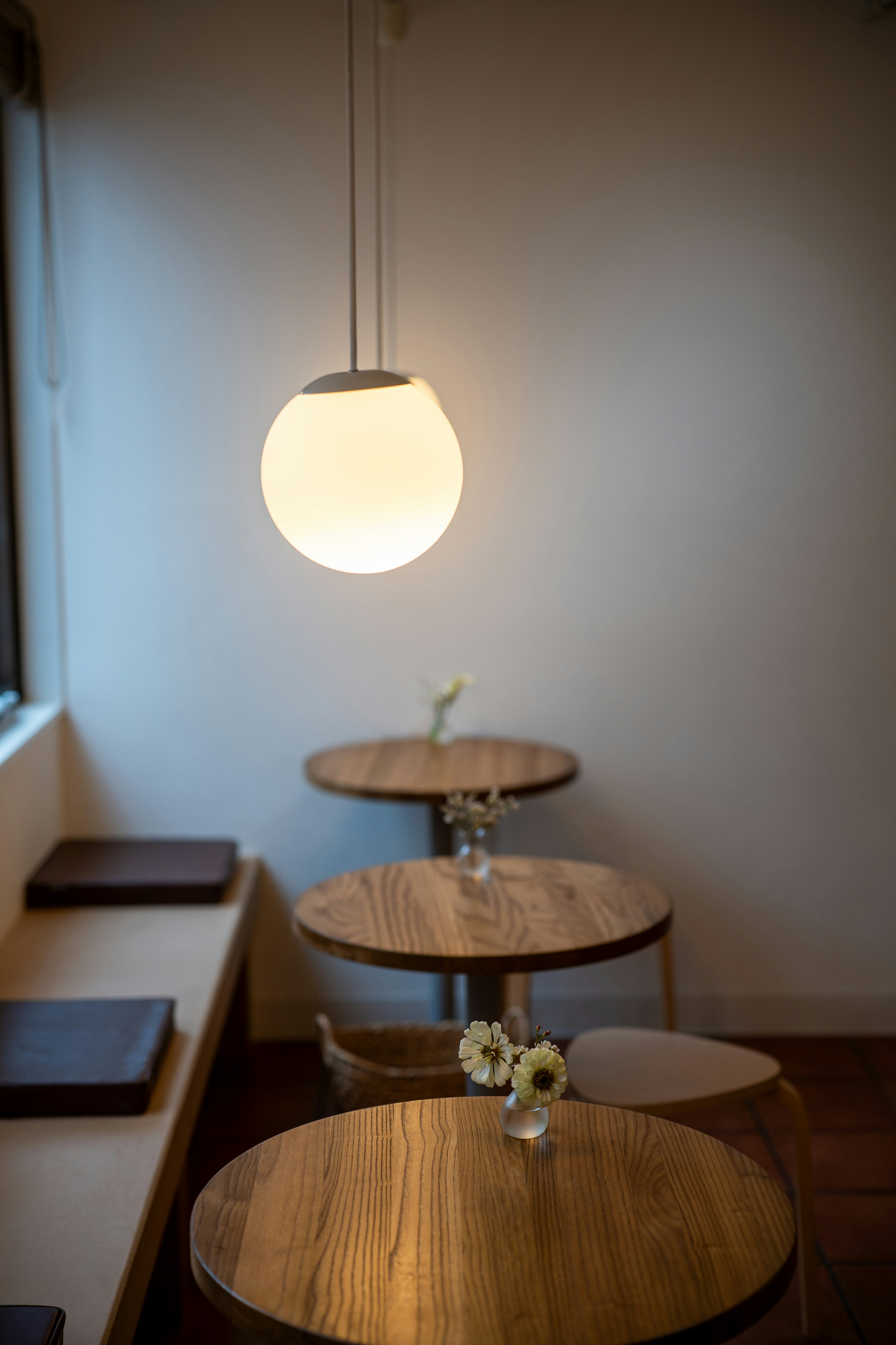 Minimalist café interior featuring a glowing pendant light and wooden tables adorned with delicate floral arrangements.