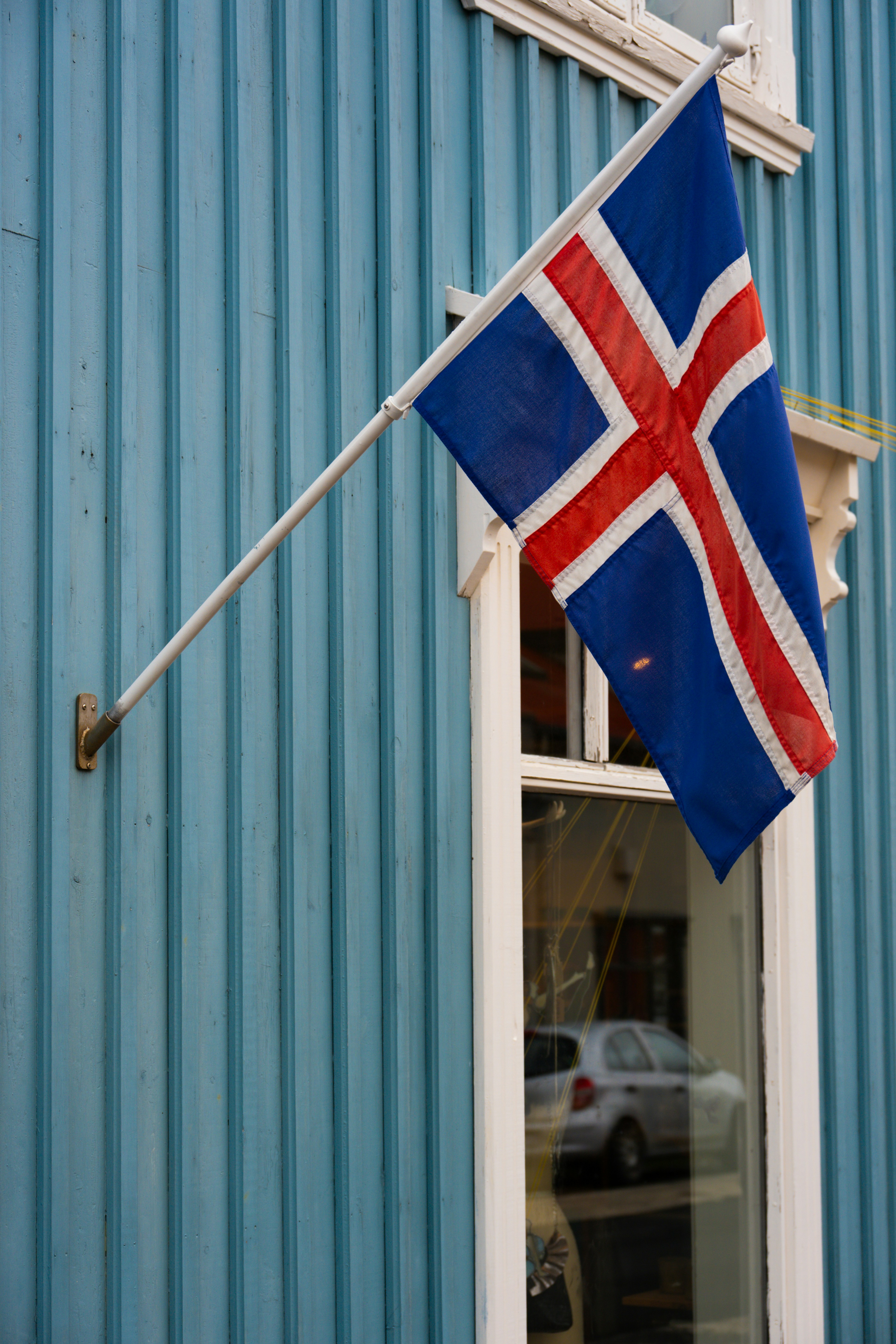 Icelandic flag fluttering beside a blue wooden building, highlighting national pride and architectural charm.
