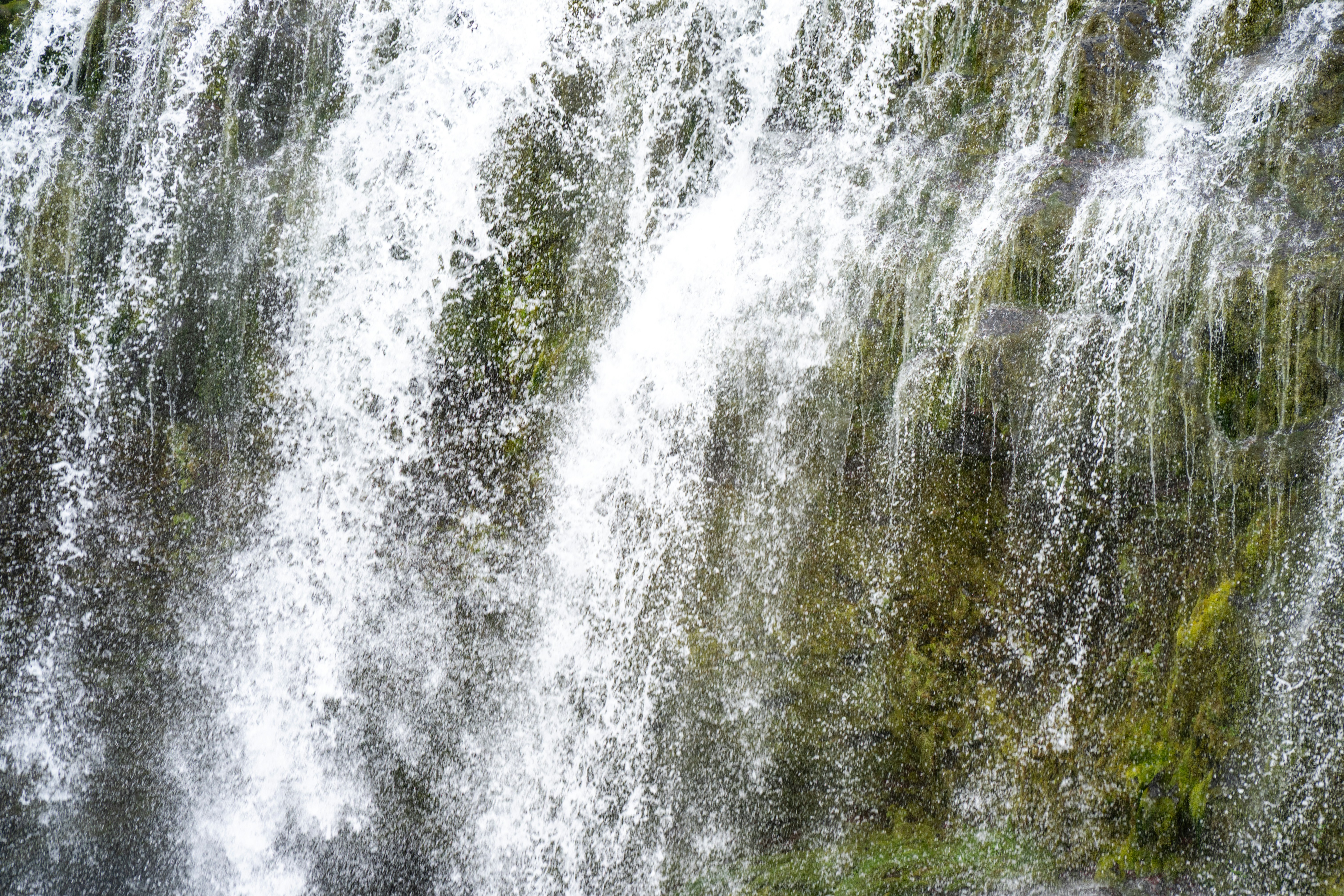A close-up view of a waterfall, showcasing the intricate patterns of water as it tumbles over moss-covered rocks. The dynamic motion creates a misty ambiance.