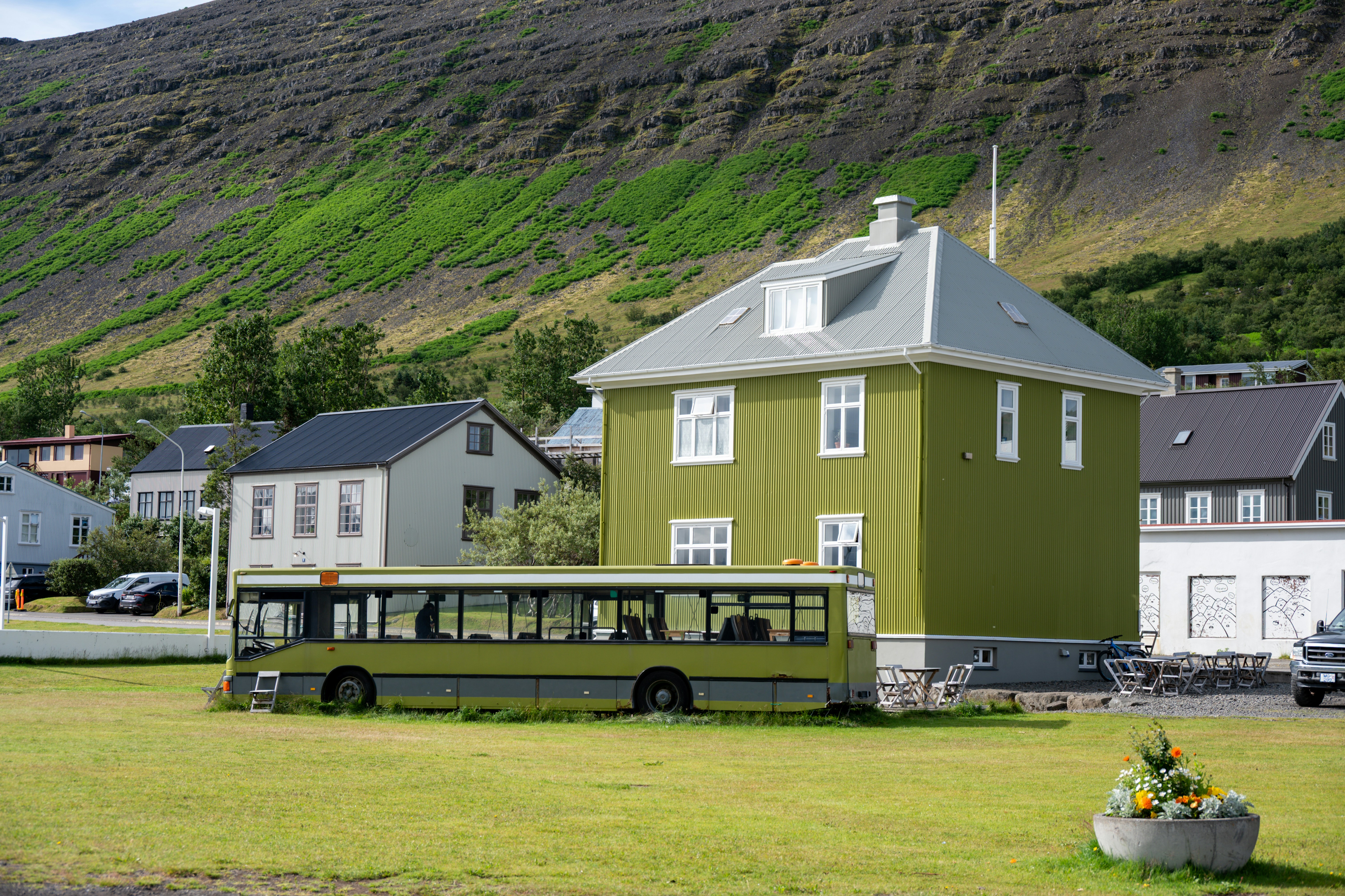 Green house and bus in front of grassy hill