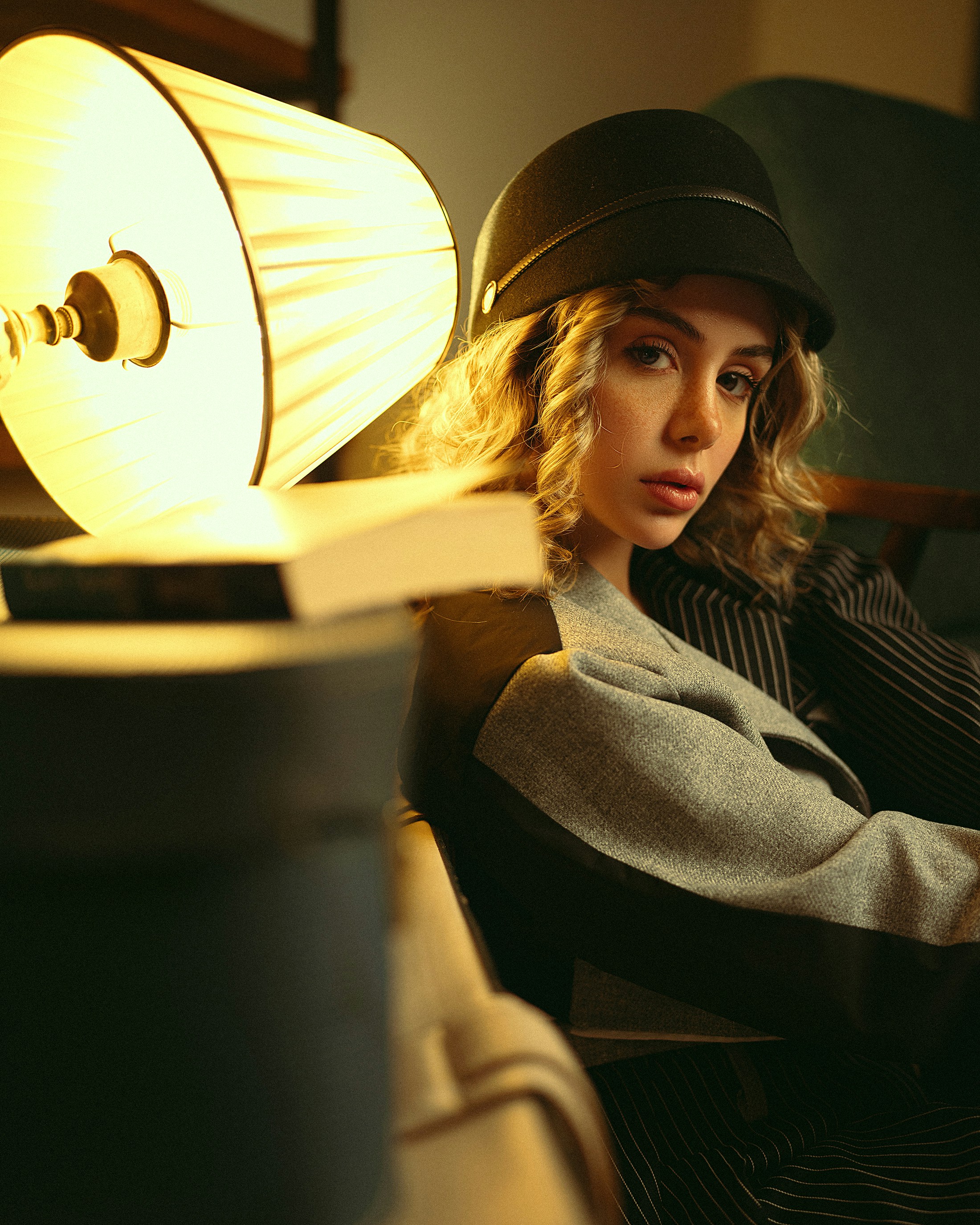 Woman in hat sits near lamp and books