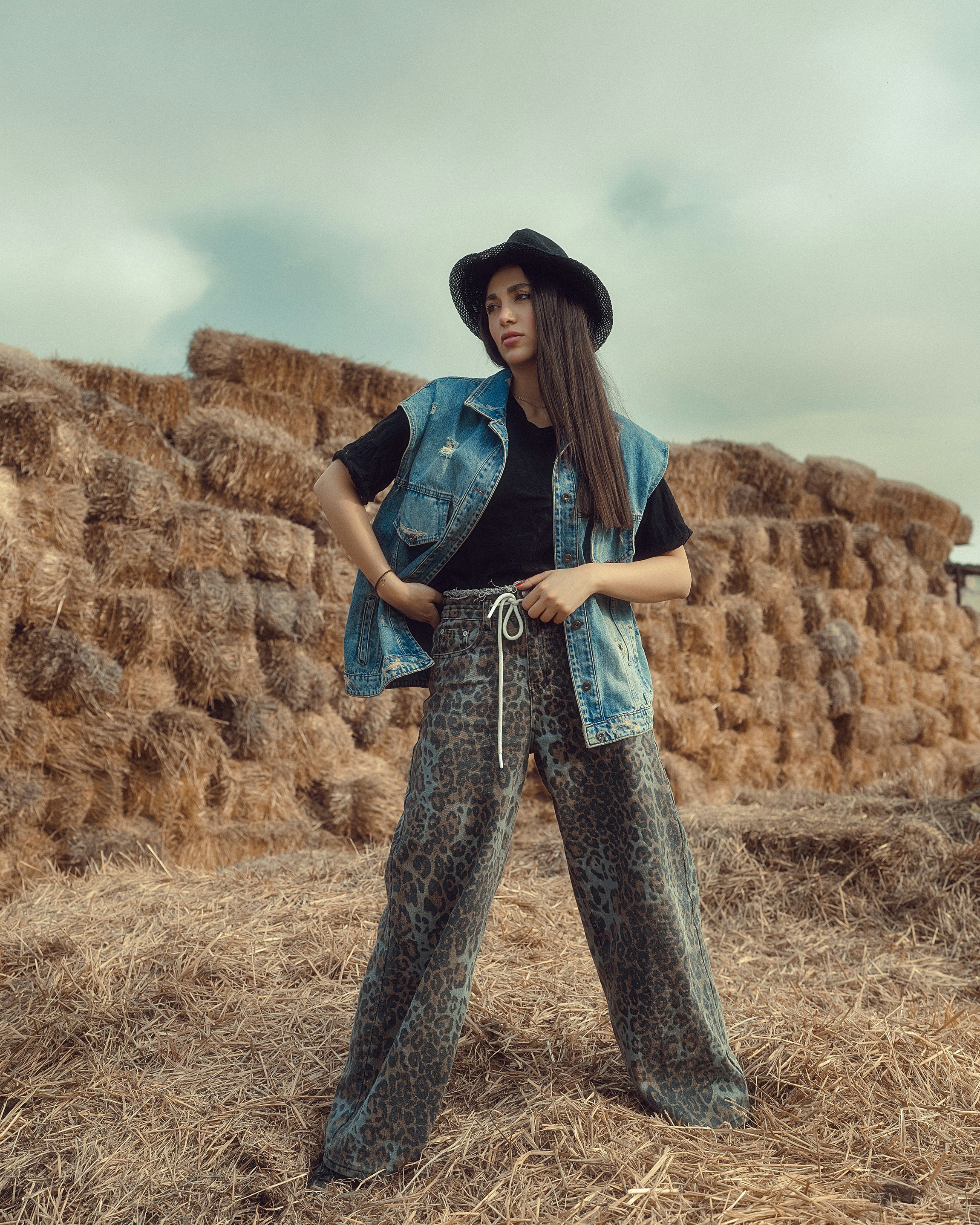 Woman in denim vest and patterned pants near hay bales