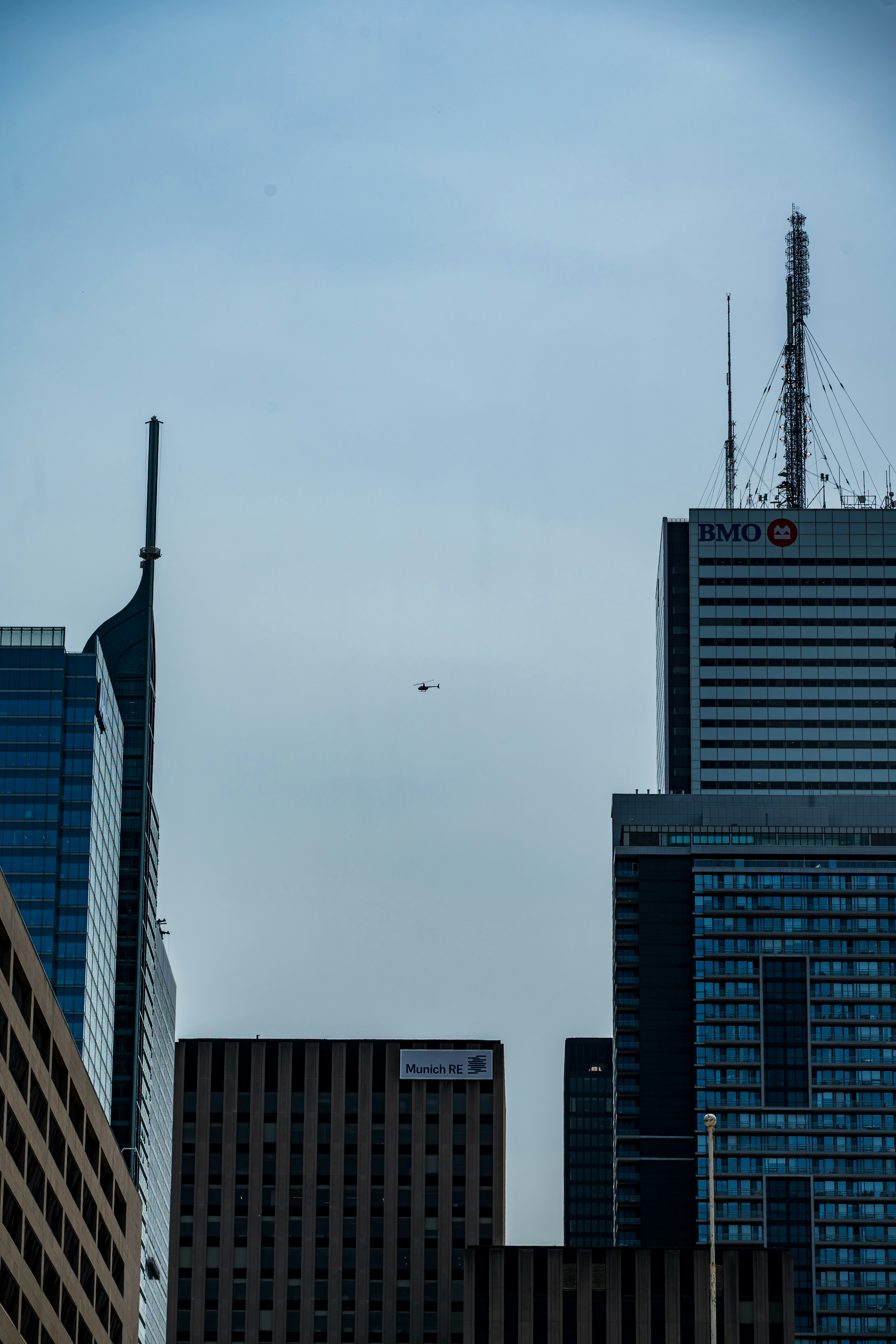 A helicopter hovers above towering skyscrapers in a bustling cityscape, highlighting the contrast between architecture and aerial movement.