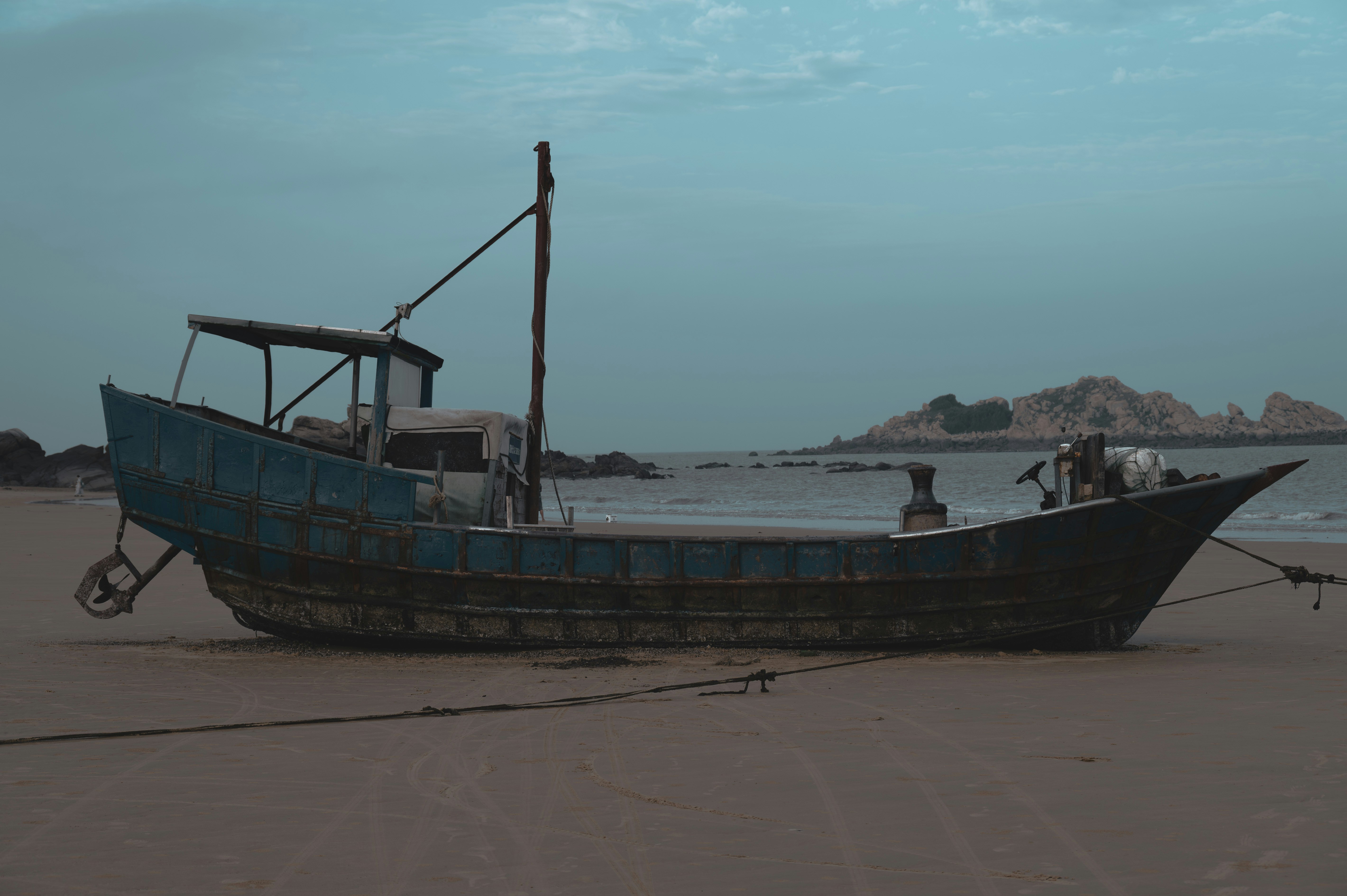 A weathered fishing boat rests on a sandy shore.