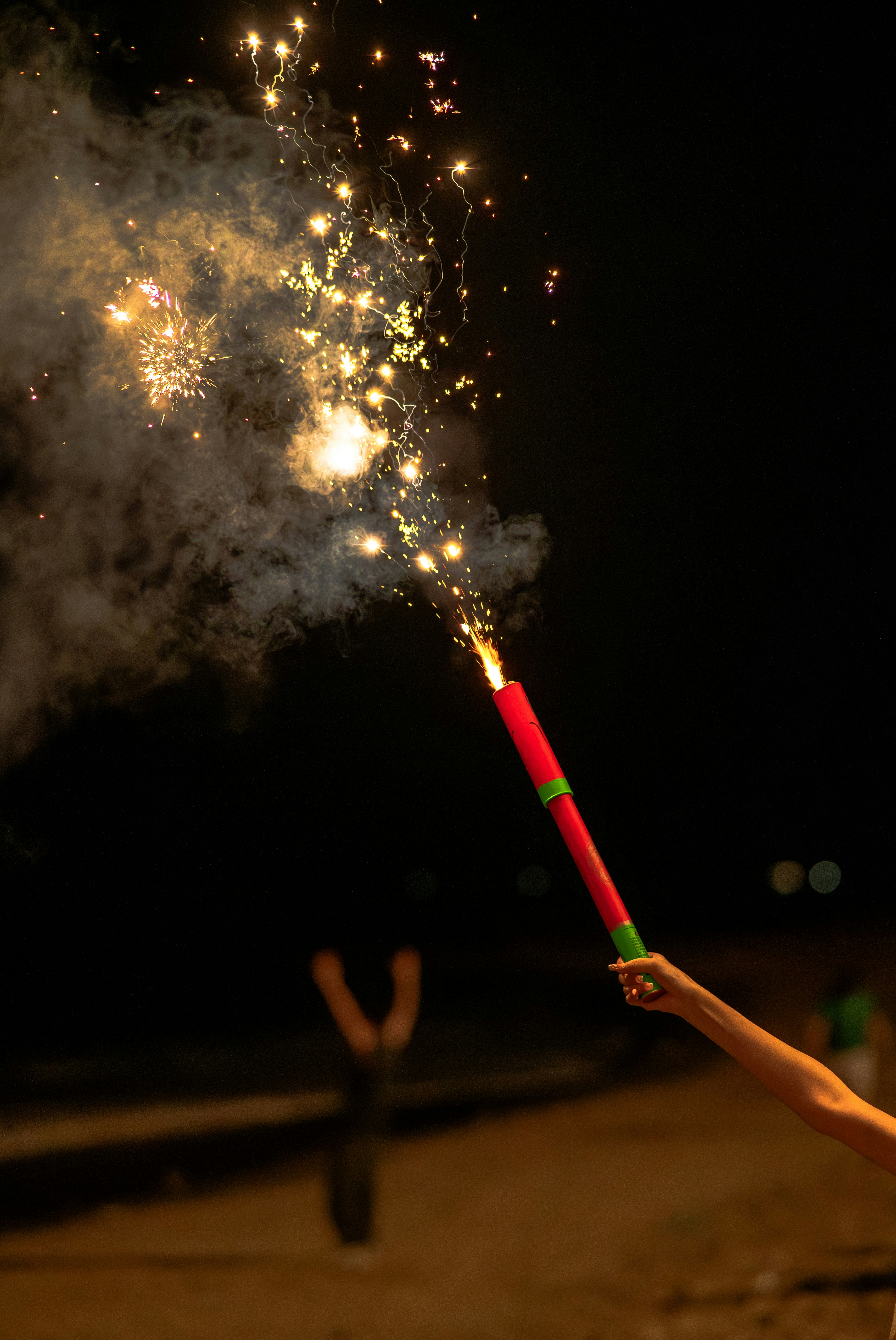 Hand holding a sparkler at night with fireworks