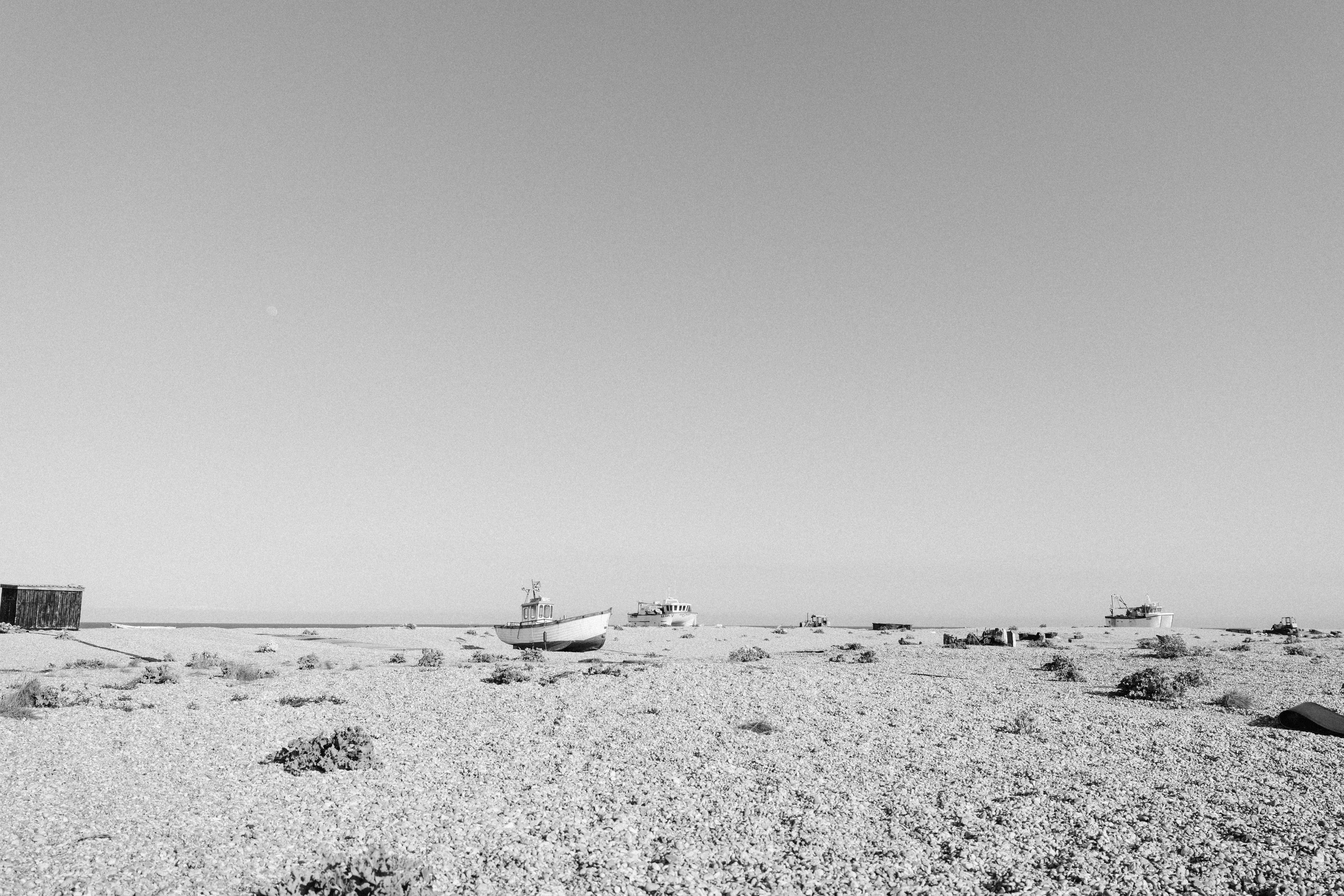 Several boats rest on a pebble beach under a clear sky.