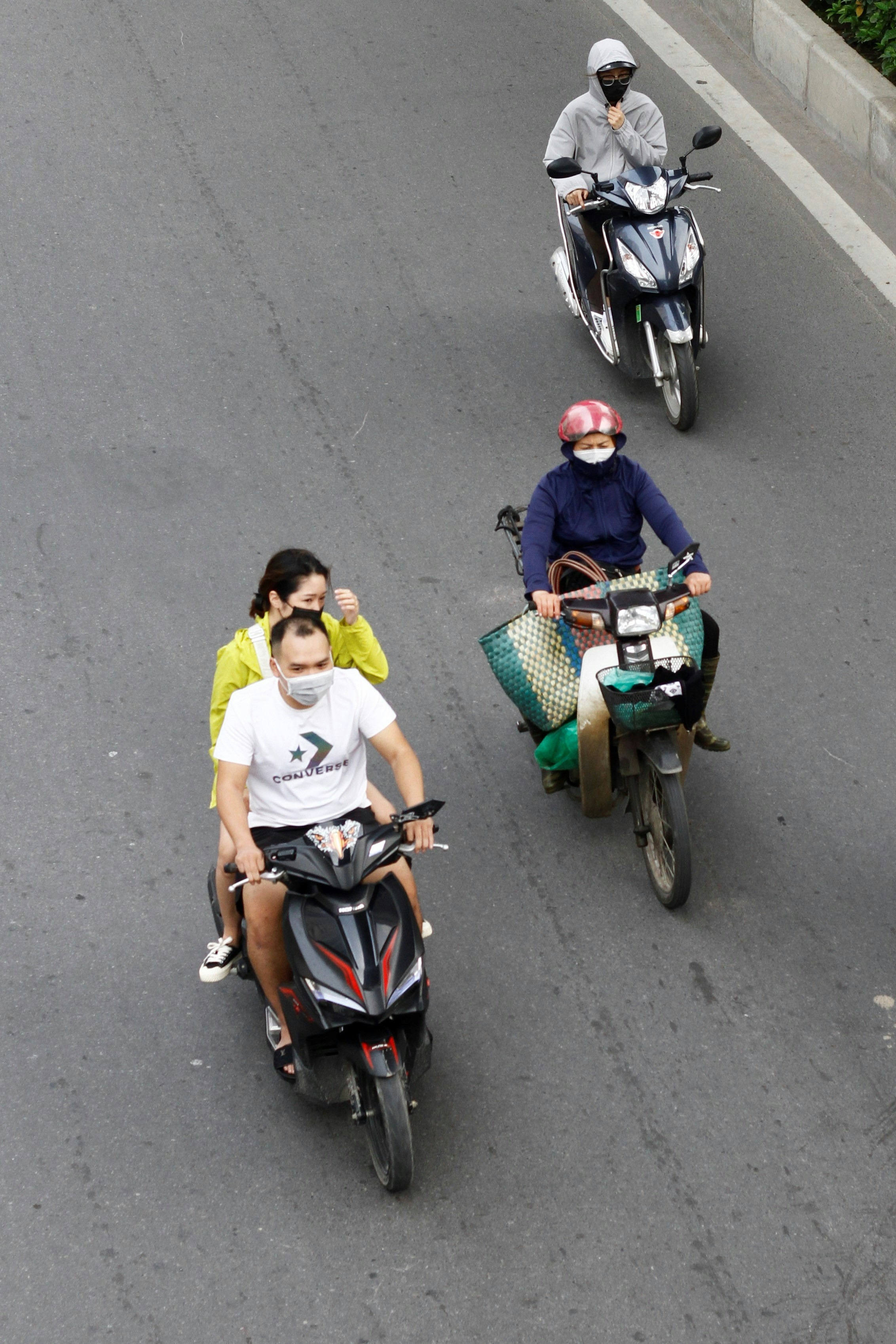 Motorbikes in Hanoi, Vietnam | Three motorcycles ride on a paved road.