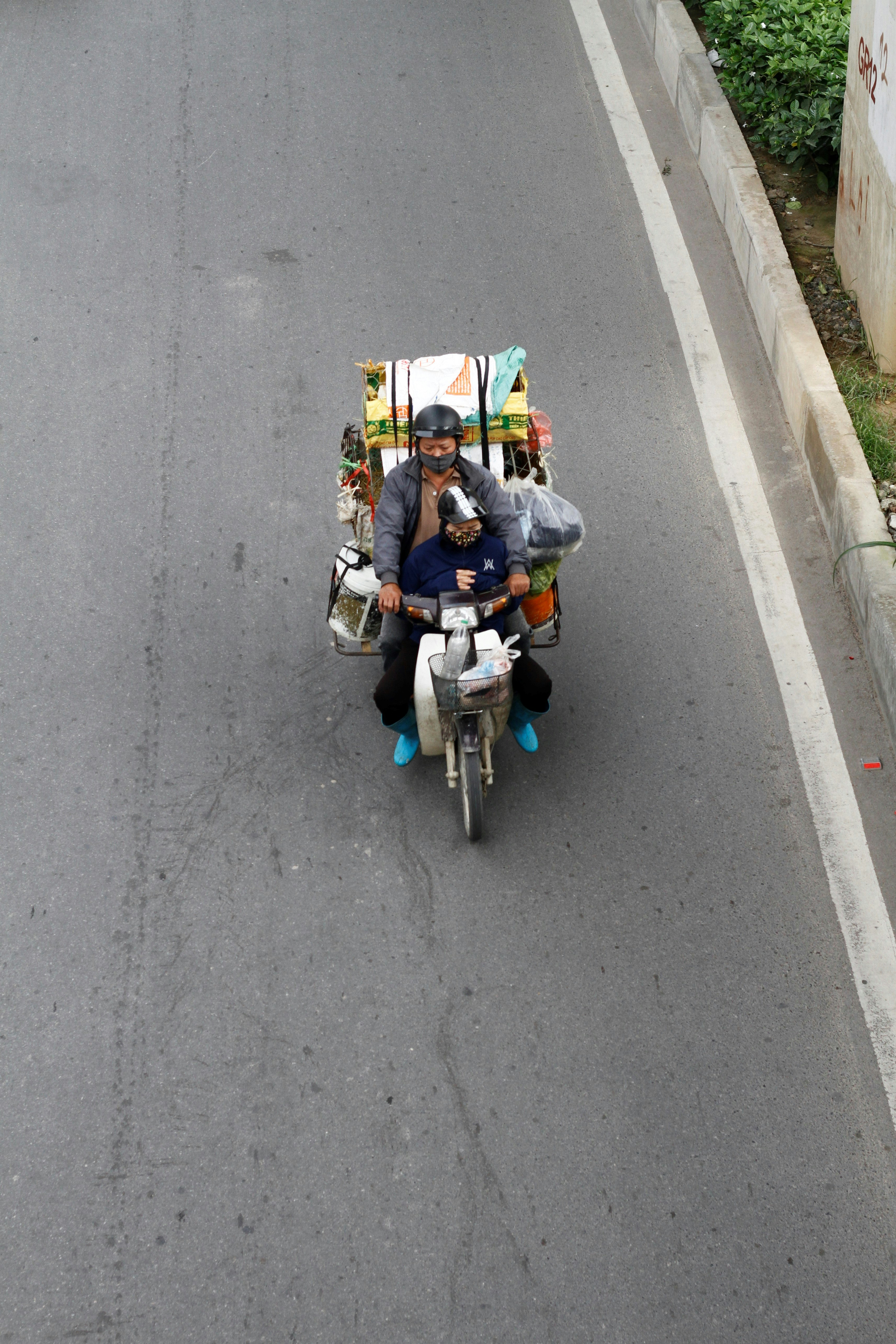 Two individuals riding a motorcycle loaded with goods on a busy street, showcasing urban transport dynamics.