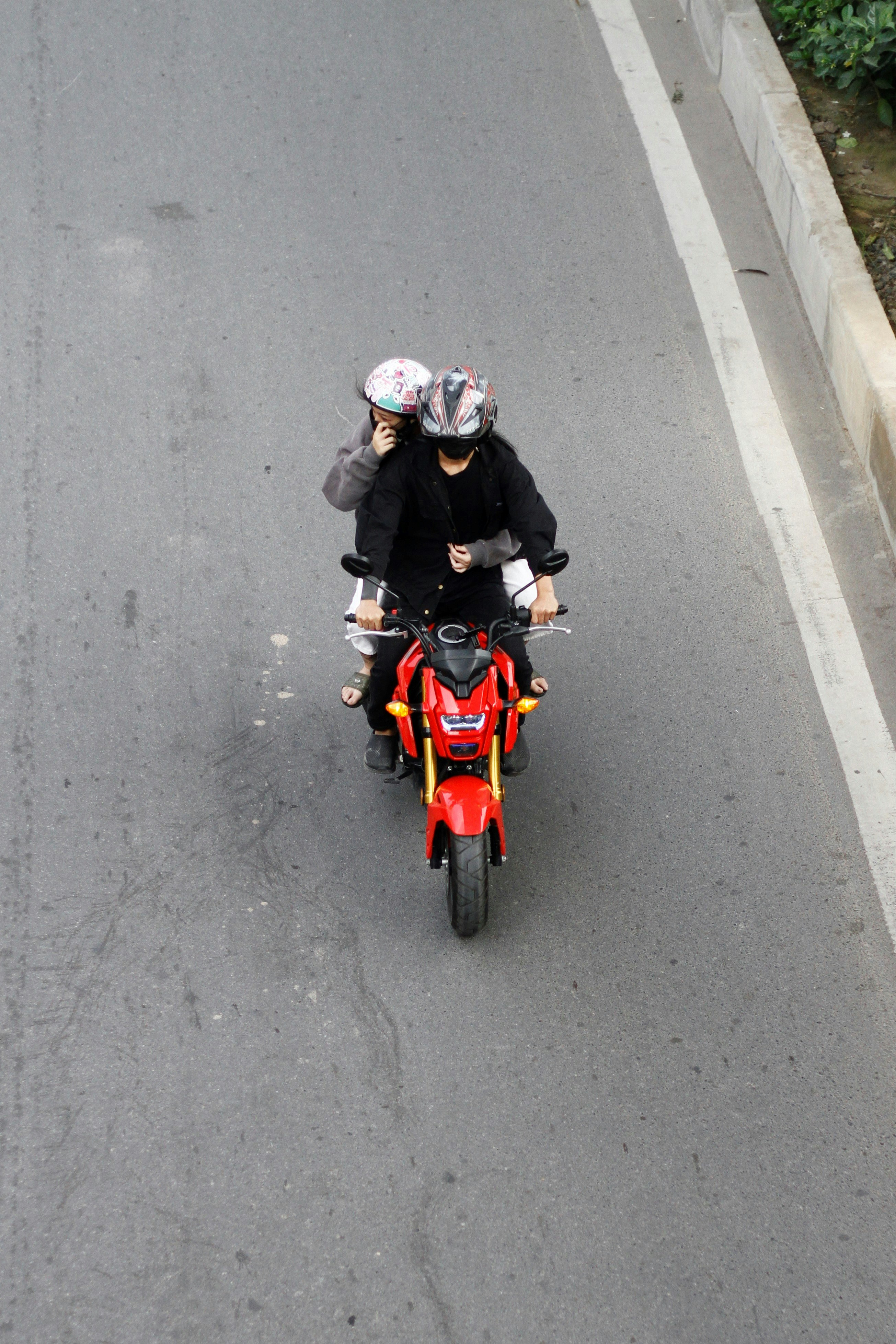 Two riders on a red motorcycle navigate an urban street, showcasing the essence of city life and camaraderie.