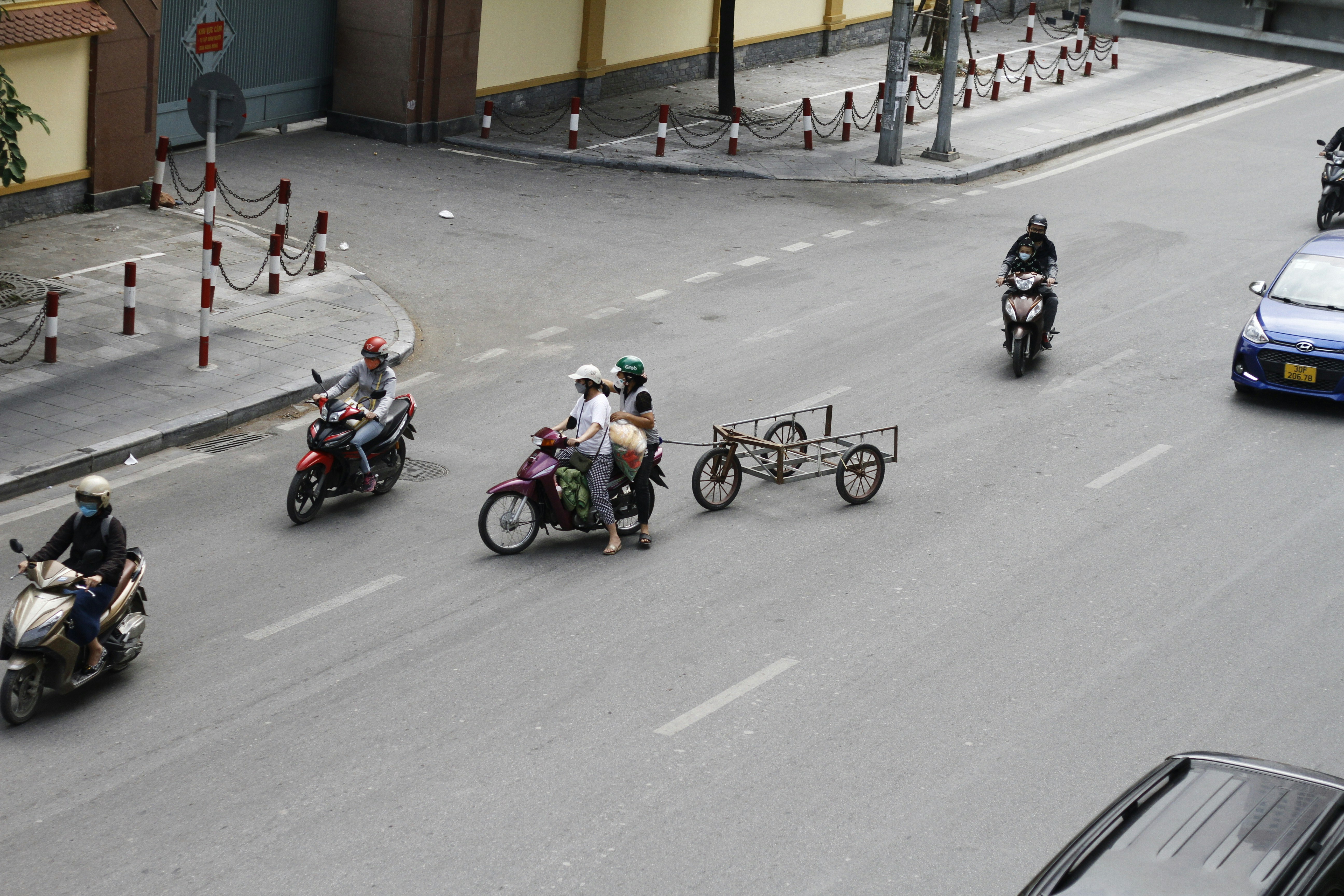 Motorbikes navigate a bustling city street, with a cart being towed in the midst of urban life.