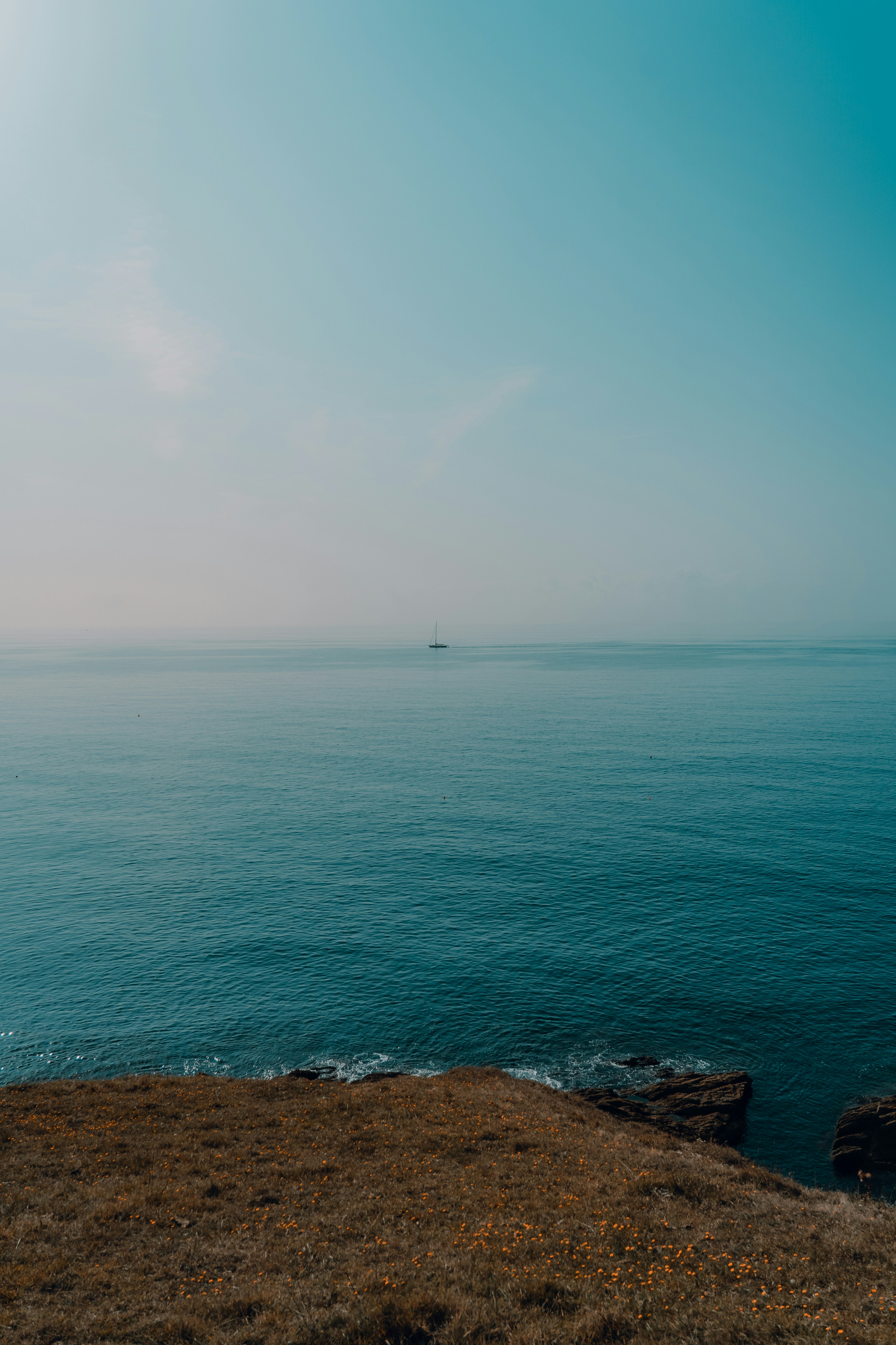 A boat in the morning haze, a mystical scene. | Calm ocean water under a hazy sky
