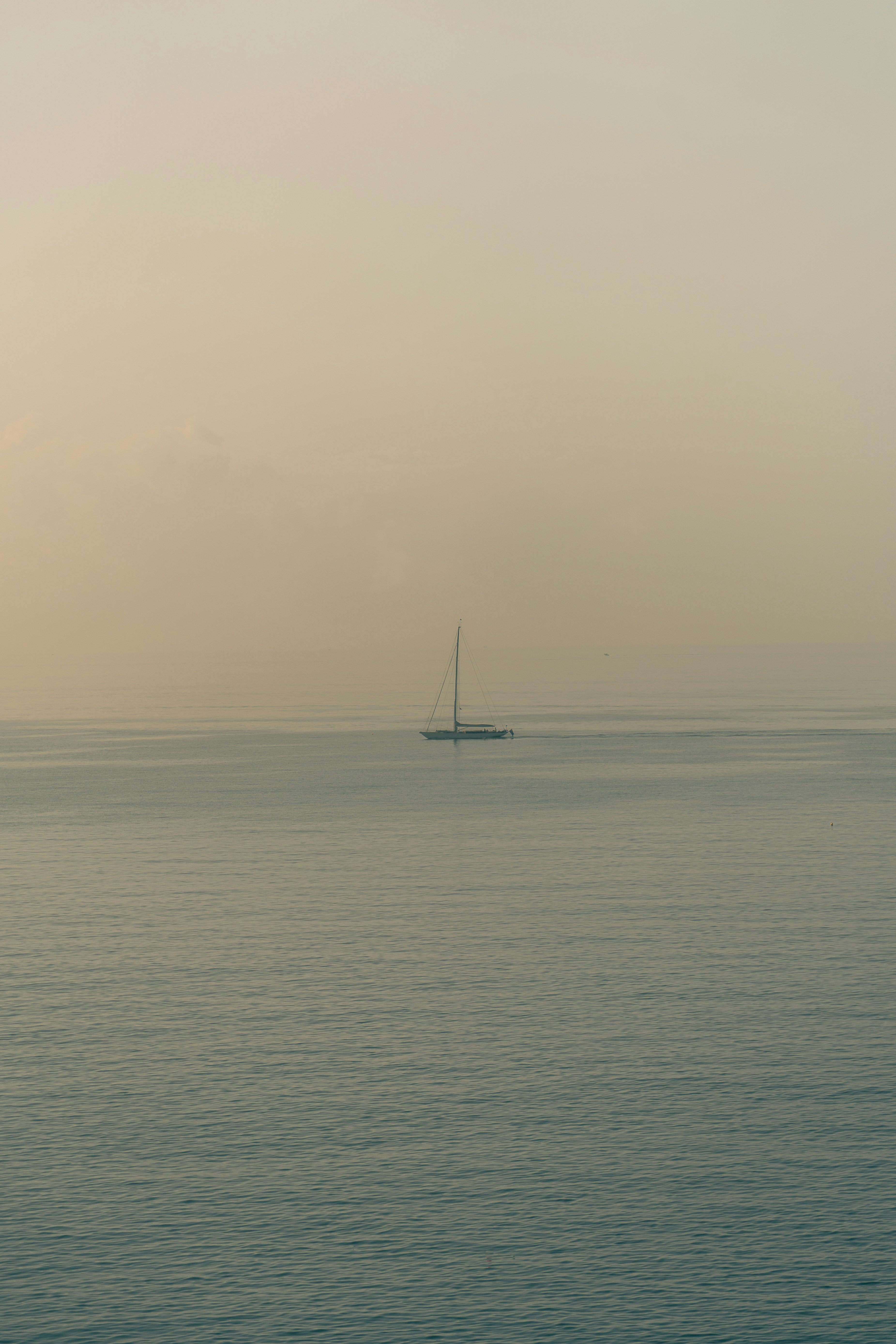 A boat in the morning haze, a mystical scene. | Sailboat on the horizon at sunset