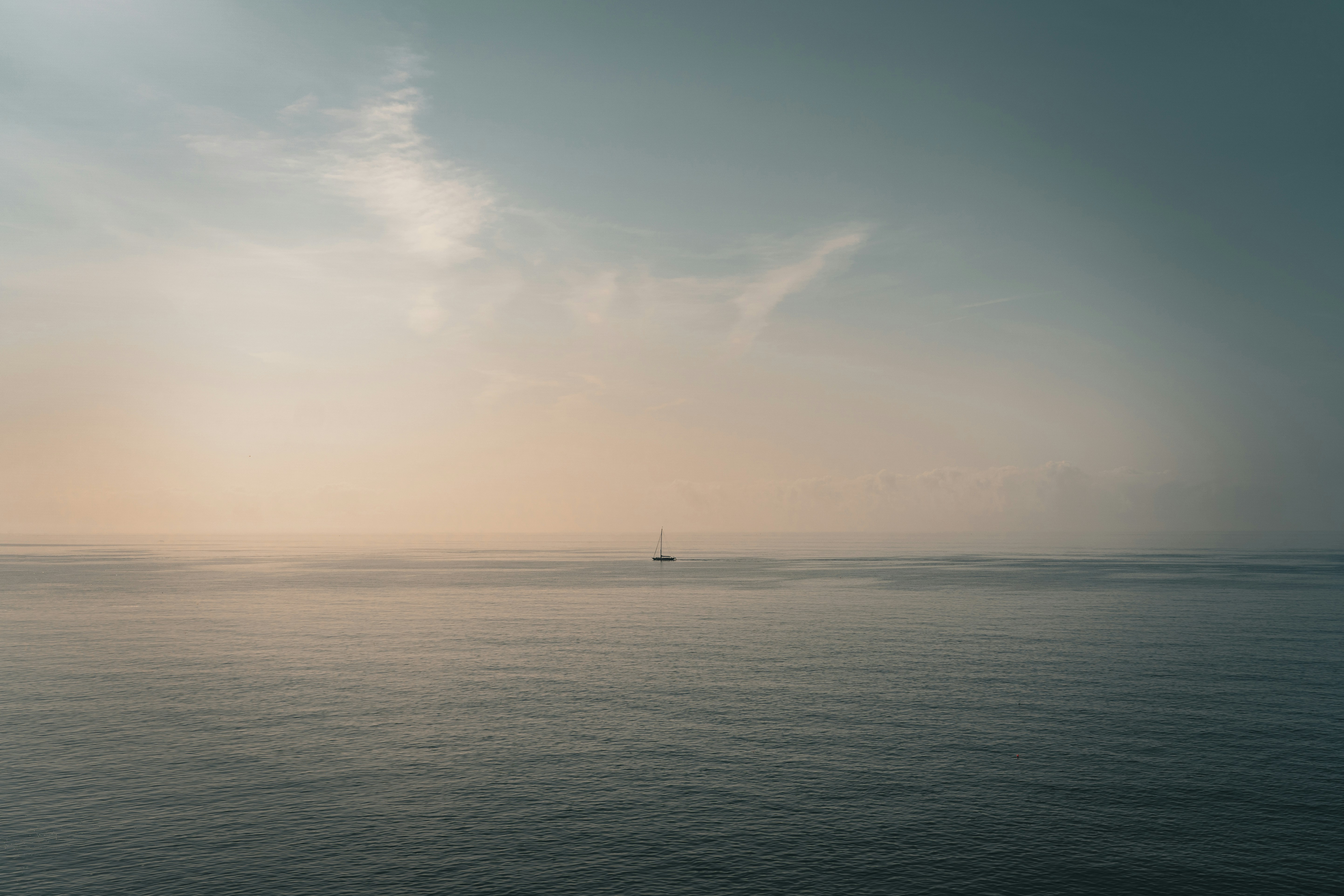 A boat in the morning haze, a mystical scene. | Calm ocean under a hazy sky at sunset