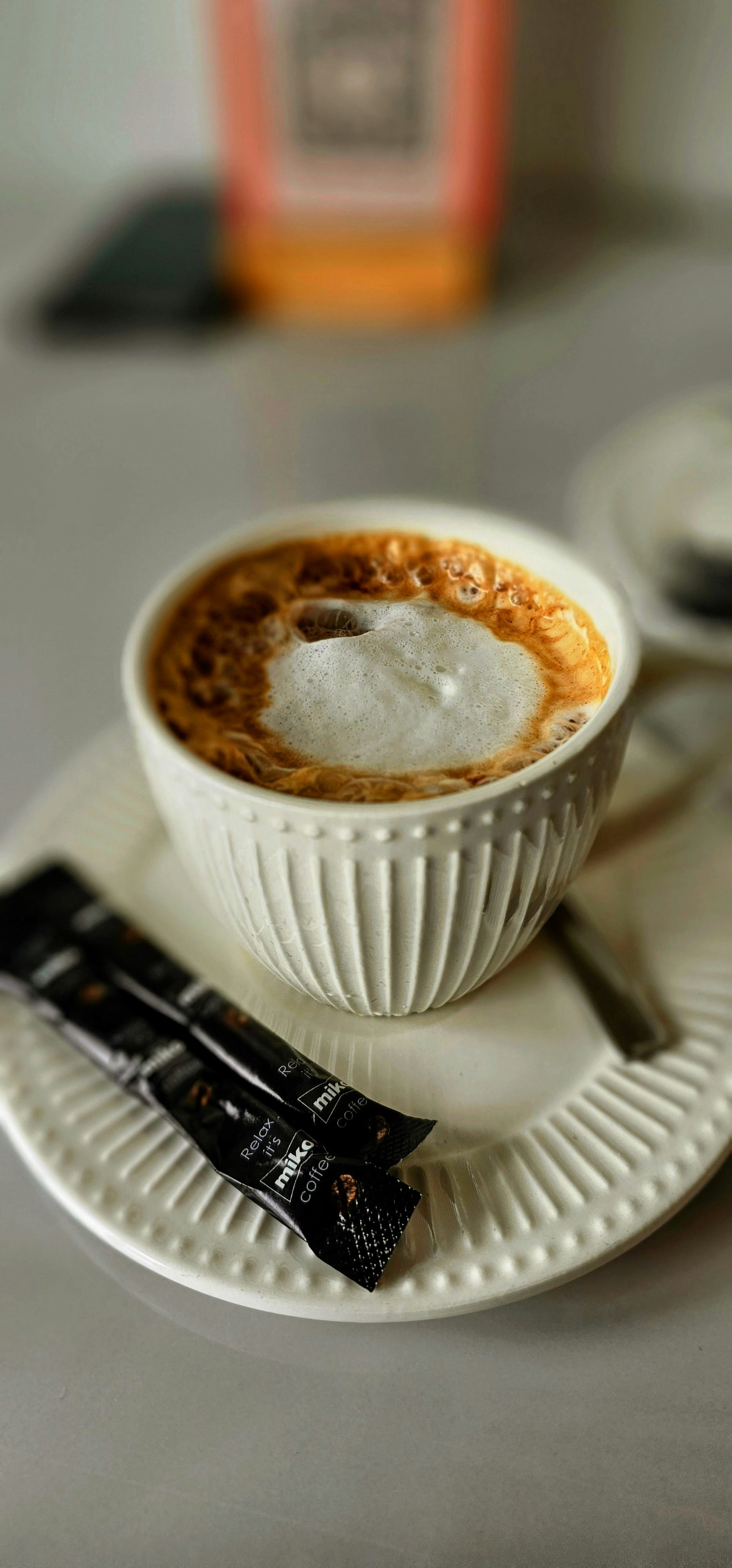 Liquid Comfort | A cup of coffee with foam and two sugar packets.