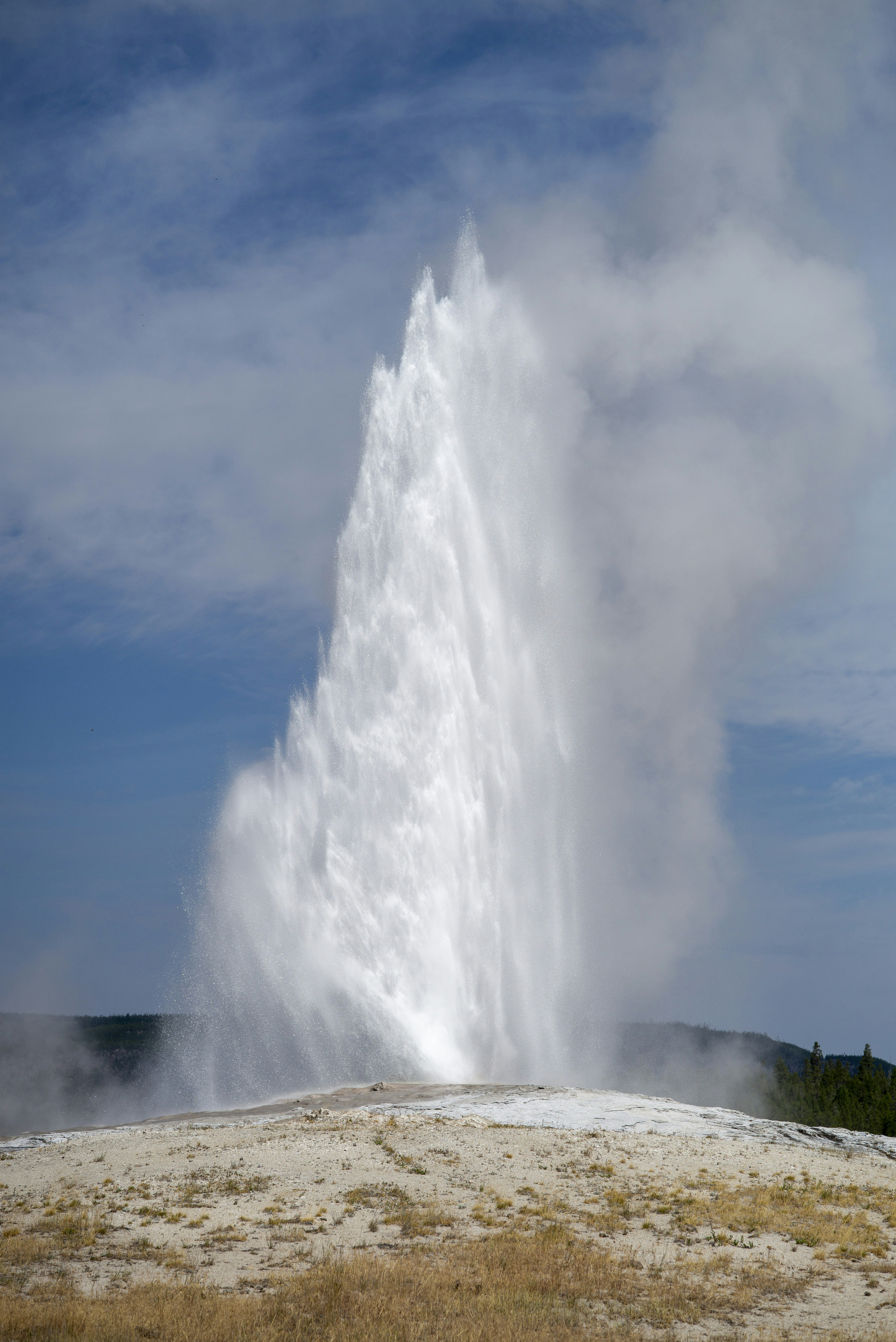 Geyser erupting with water and steam against blue sky