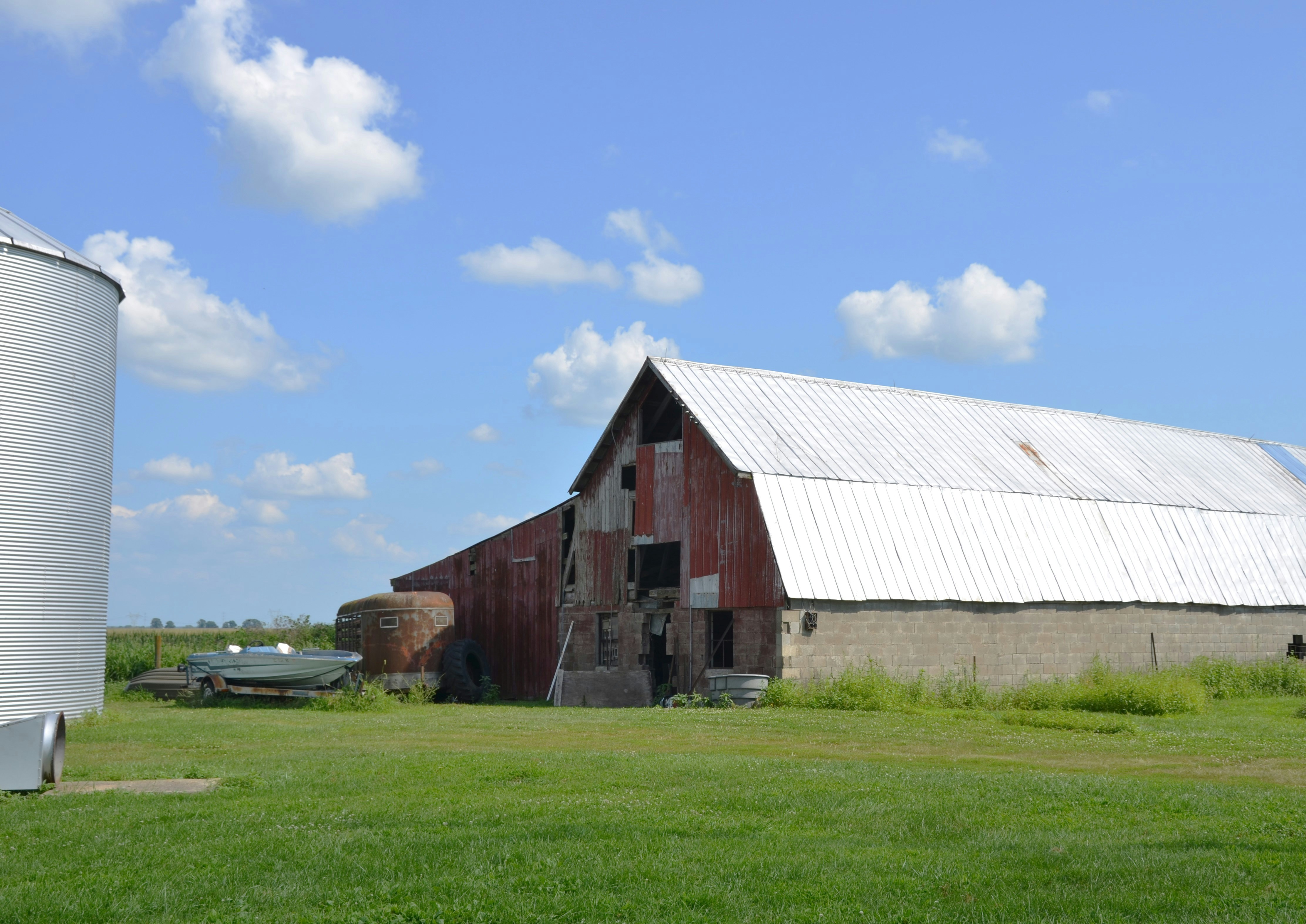 Weathered red barn stands proudly beside a silvery grain bin under a blue sky dotted with clouds.