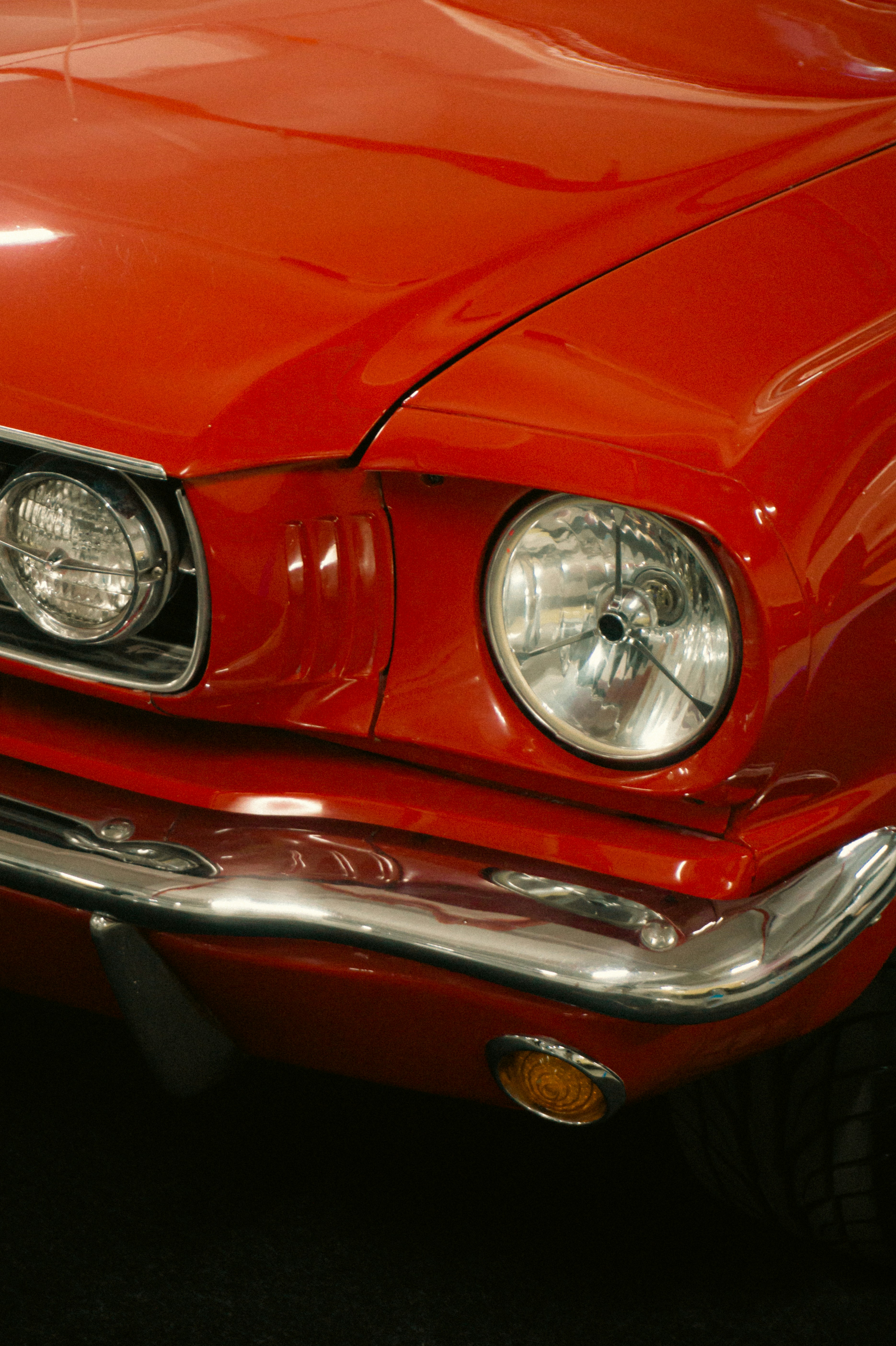Close-up of a vintage red car's front end, showcasing its iconic headlight and sleek lines.