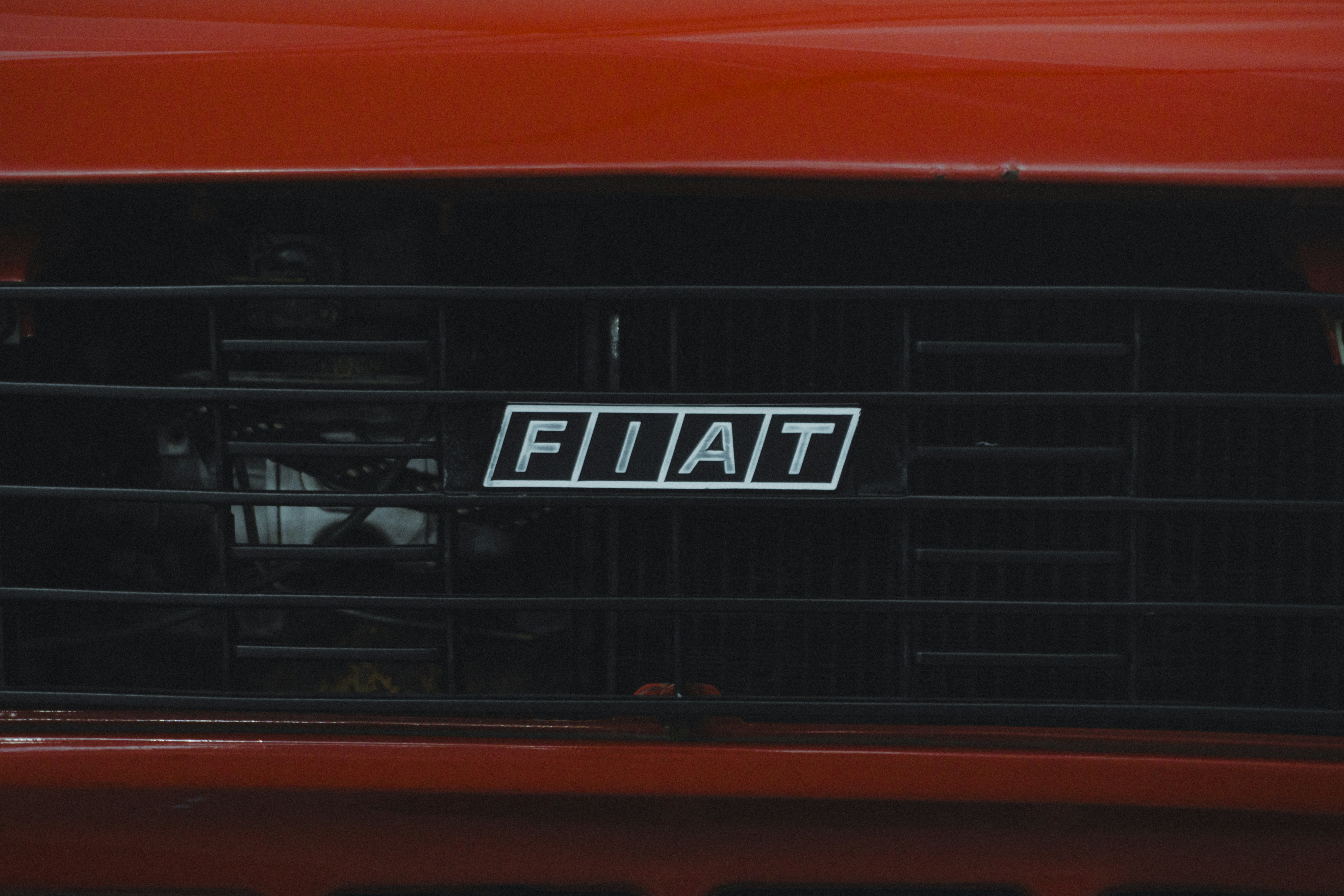 Close-up of a Fiat logo prominently displayed on a vintage car's grille, showcasing the brand's iconic design. The bold black and silver lettering contrasts against the vibrant red background.