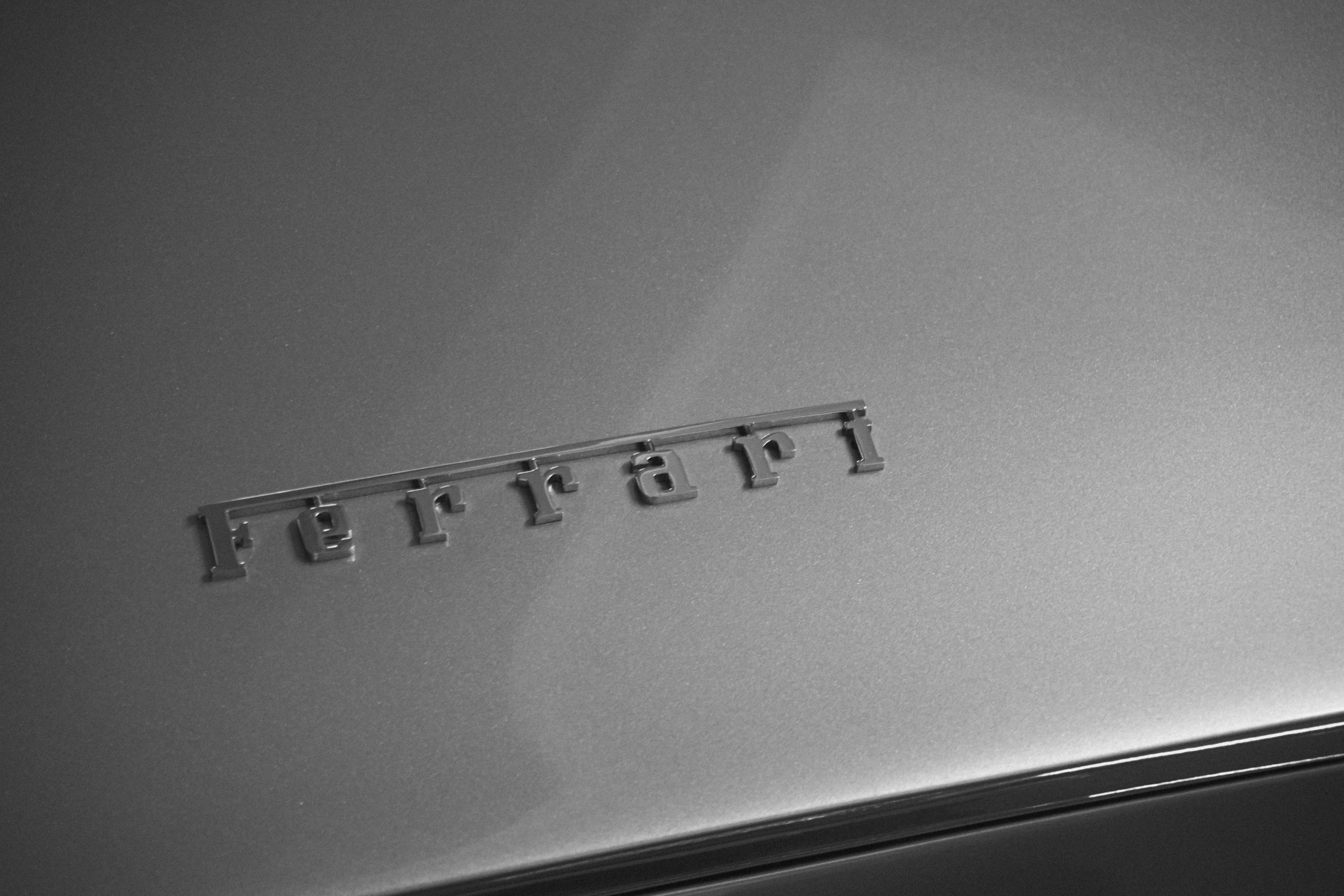 Close-up of a polished Ferrari emblem reflecting light on a sleek surface. The logo embodies luxury and automotive excellence.