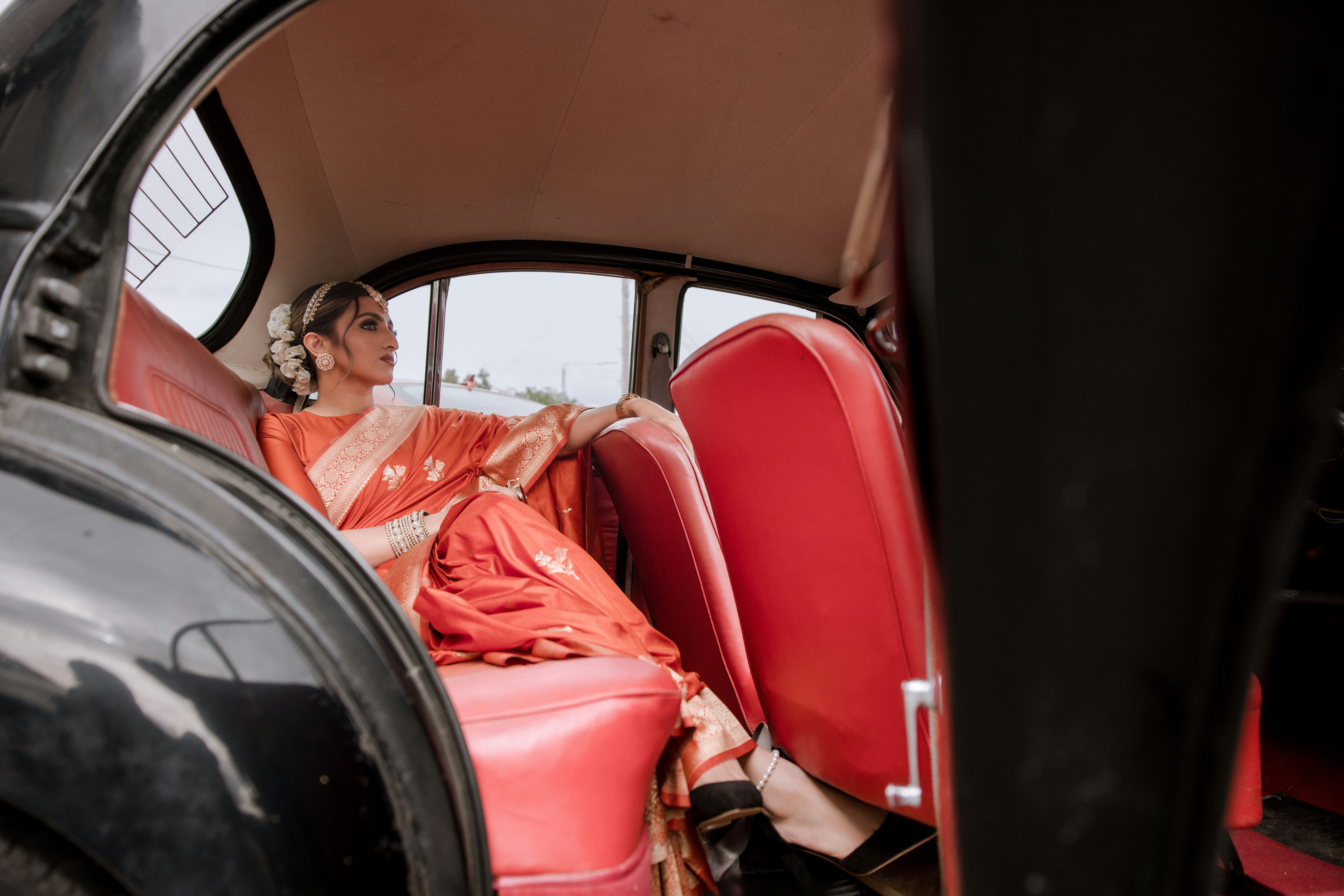 A woman in traditional attire seated gracefully in a vintage car, embodying a blend of heritage and modernity.