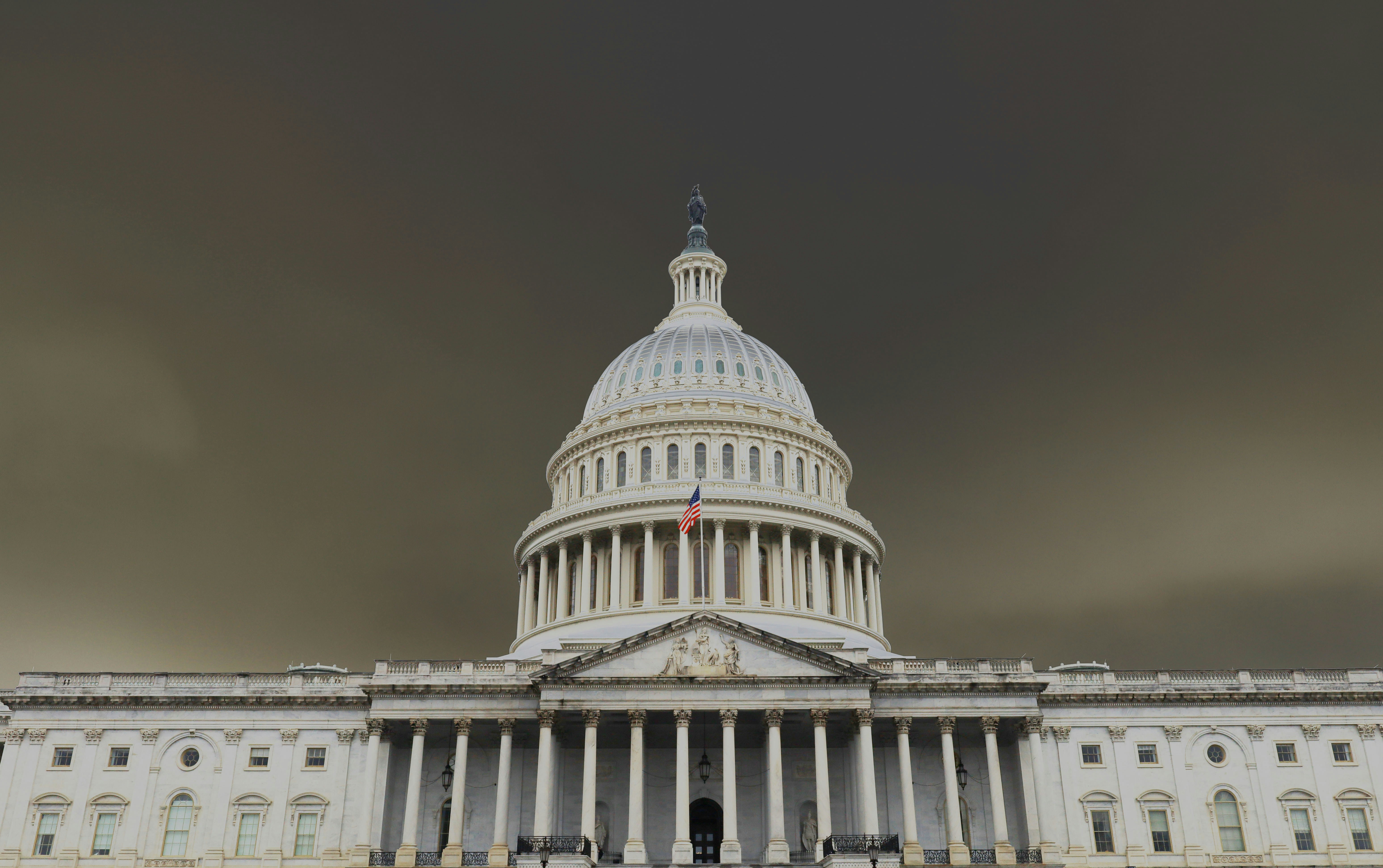 The United States Capitol stands majestically under a dramatic, dark sky, showcasing its iconic dome and classical architecture.