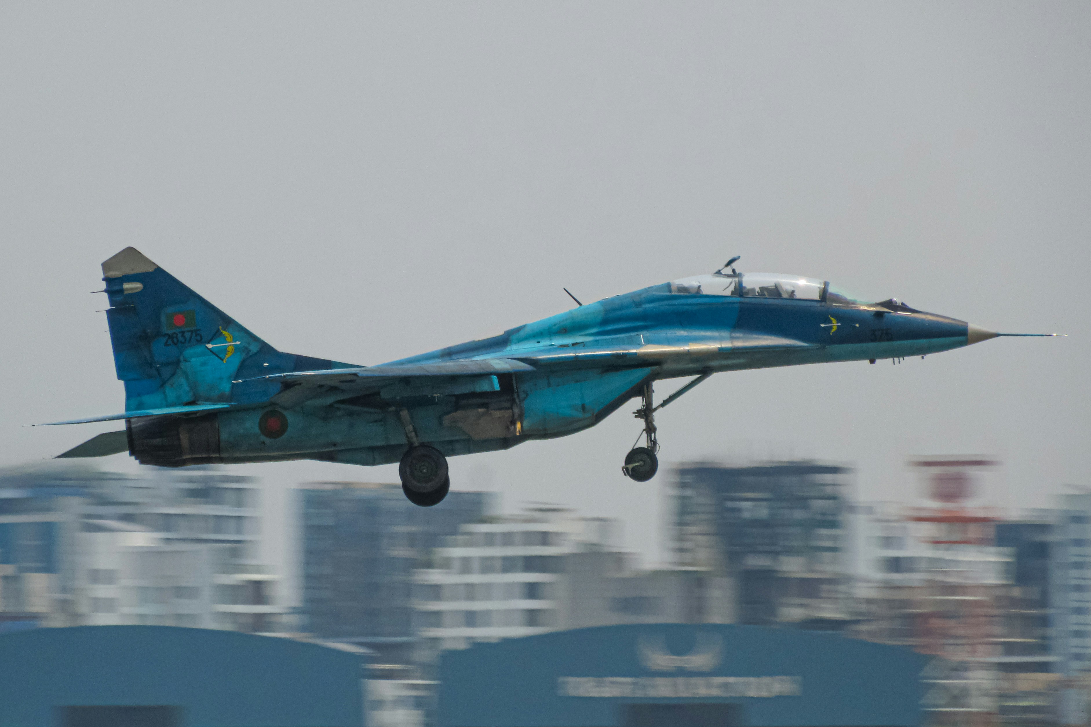 Fighter jet soaring above an urban skyline, showcasing its sleek design and vibrant colors against a backdrop of modern buildings.