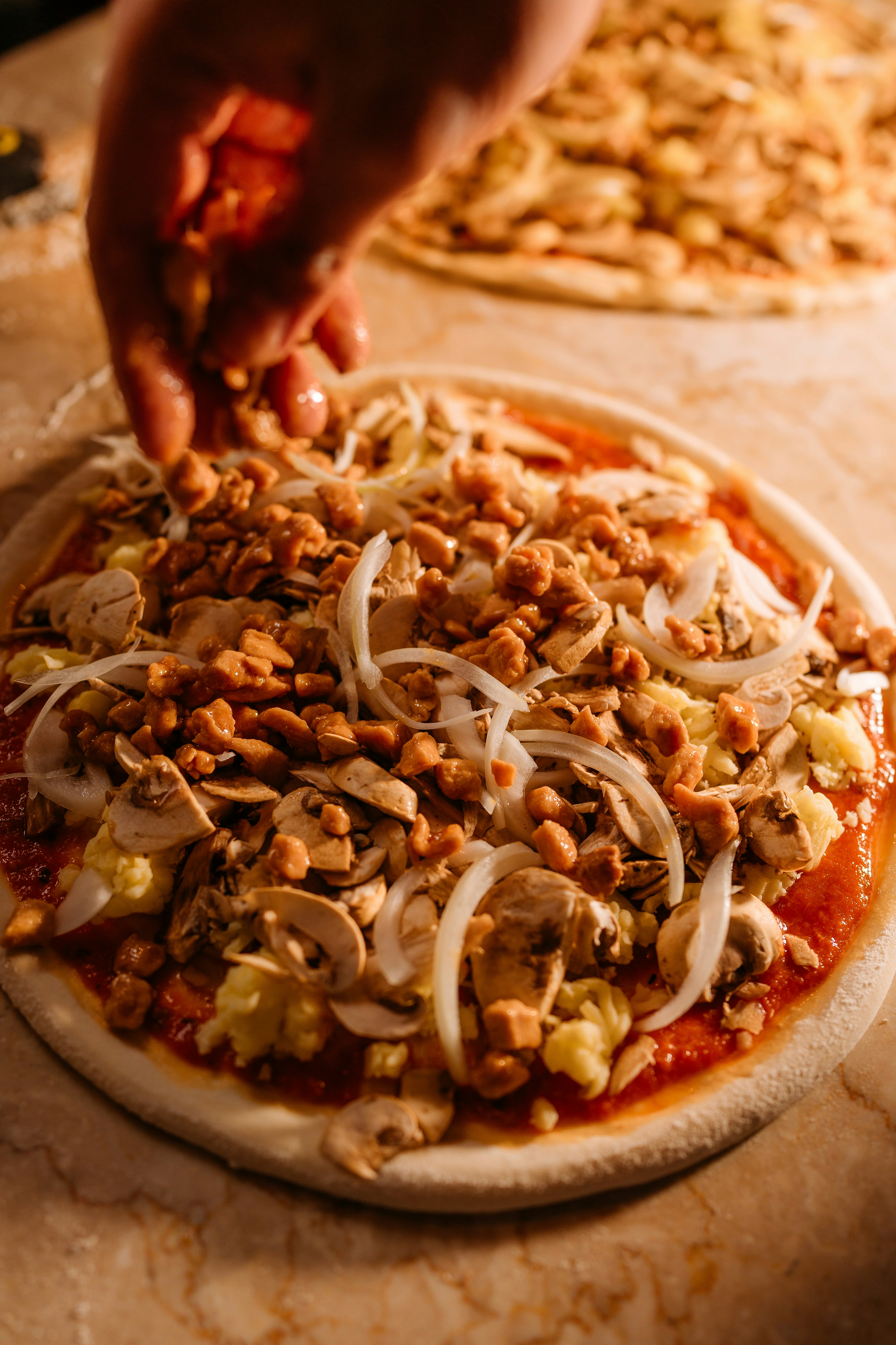 Fresh mushrooms, onions, and other toppings being added to a pizza before baking, showcasing the art of pizza-making in Gianyar, Bali. | Chef adding toppings to a pizza