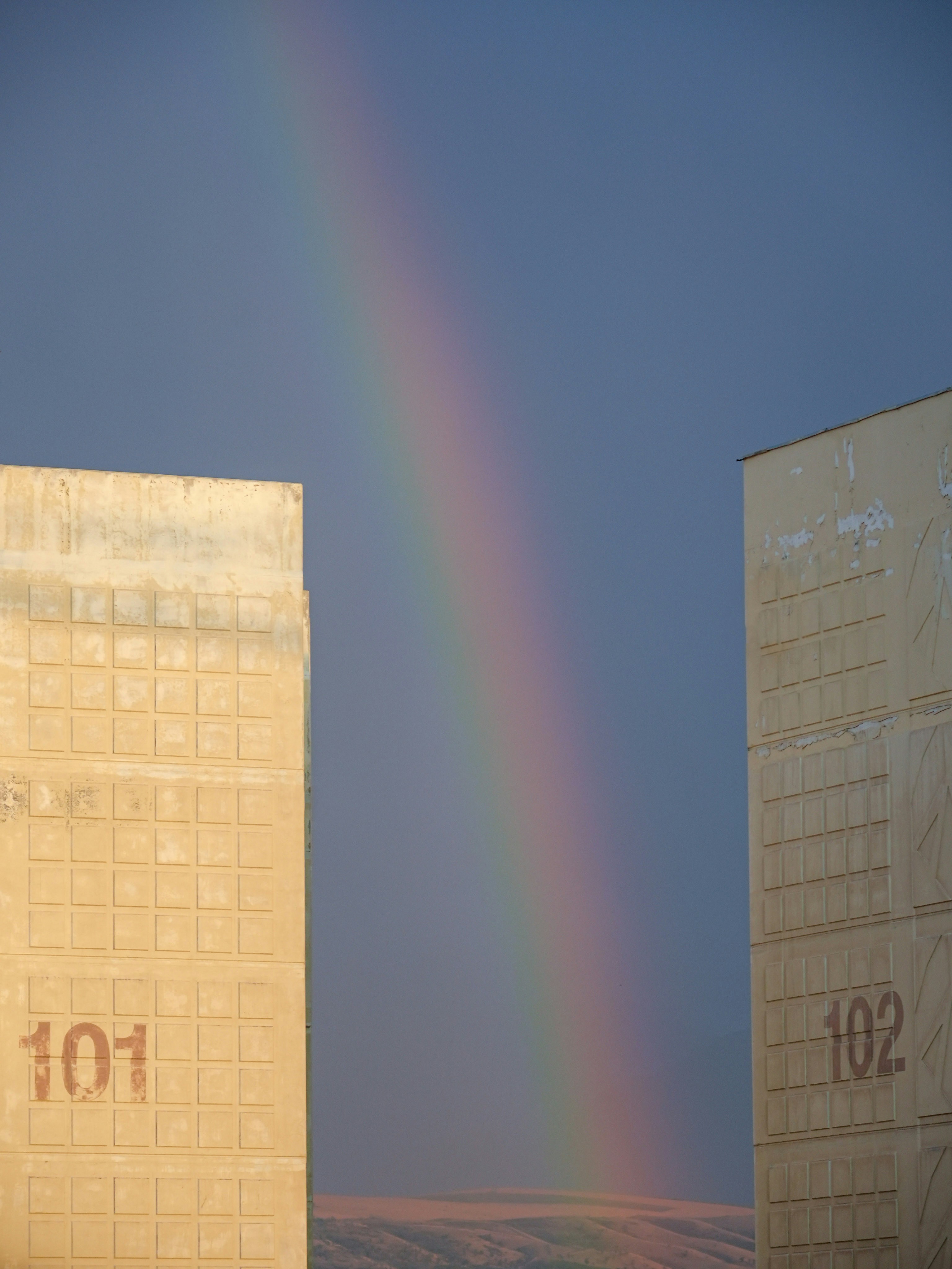 Rainbow appears between two buildings against a dark sky