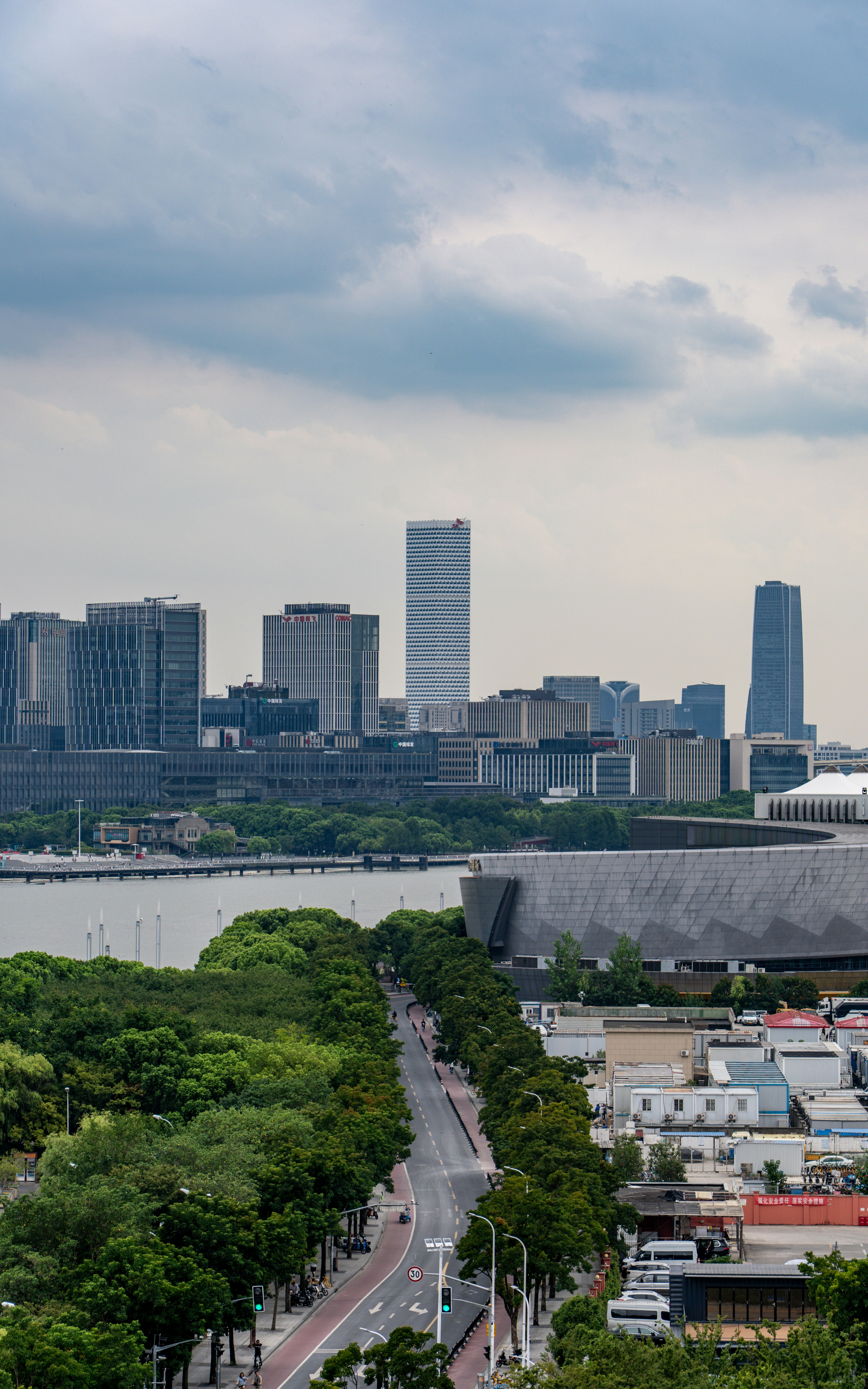 Modern cityscape with tall buildings and a tree-lined road.
