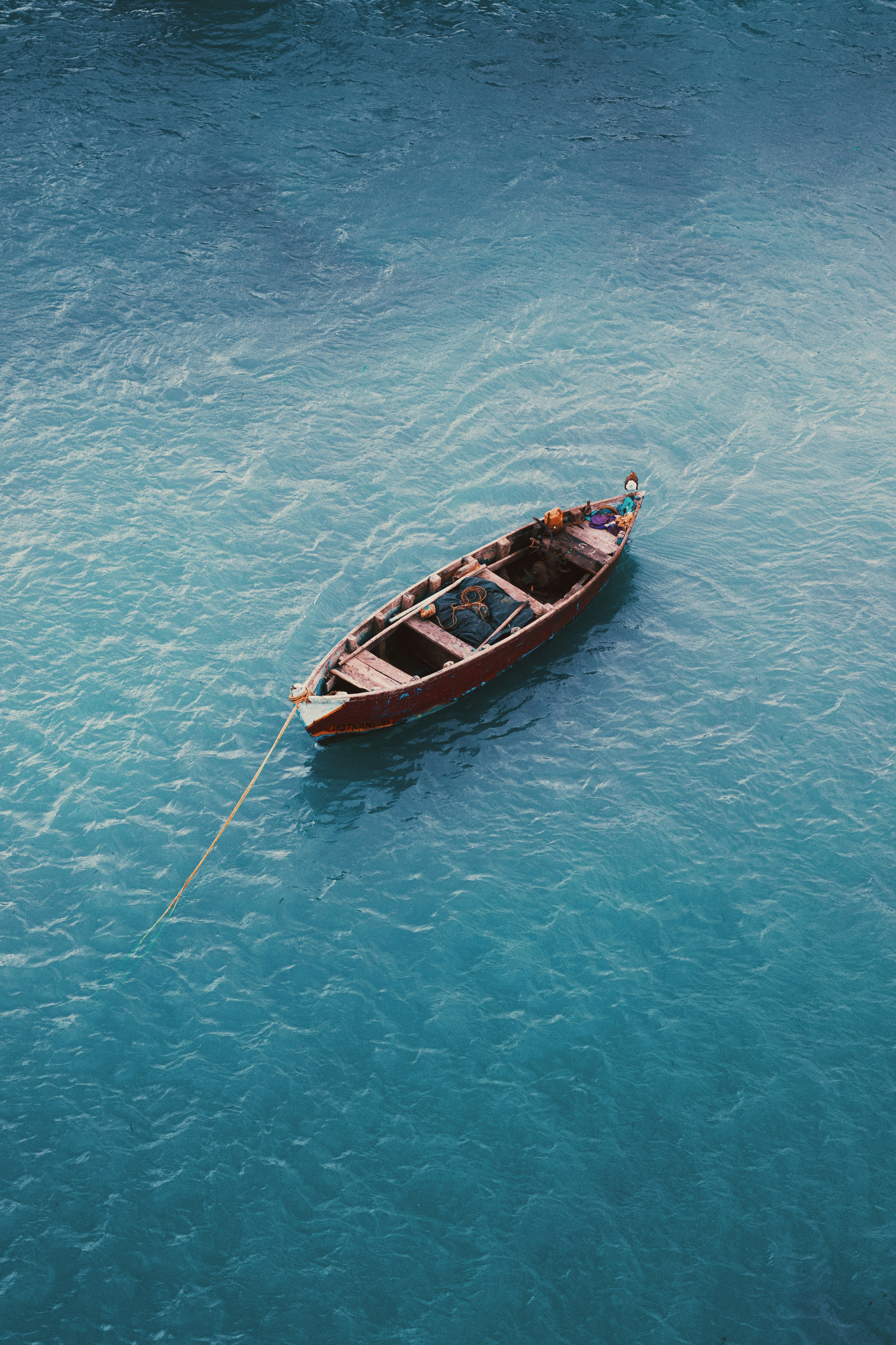 Anchored in solitude - a lone fishing boat resting on calm water. | A small wooden boat floats on calm blue water.