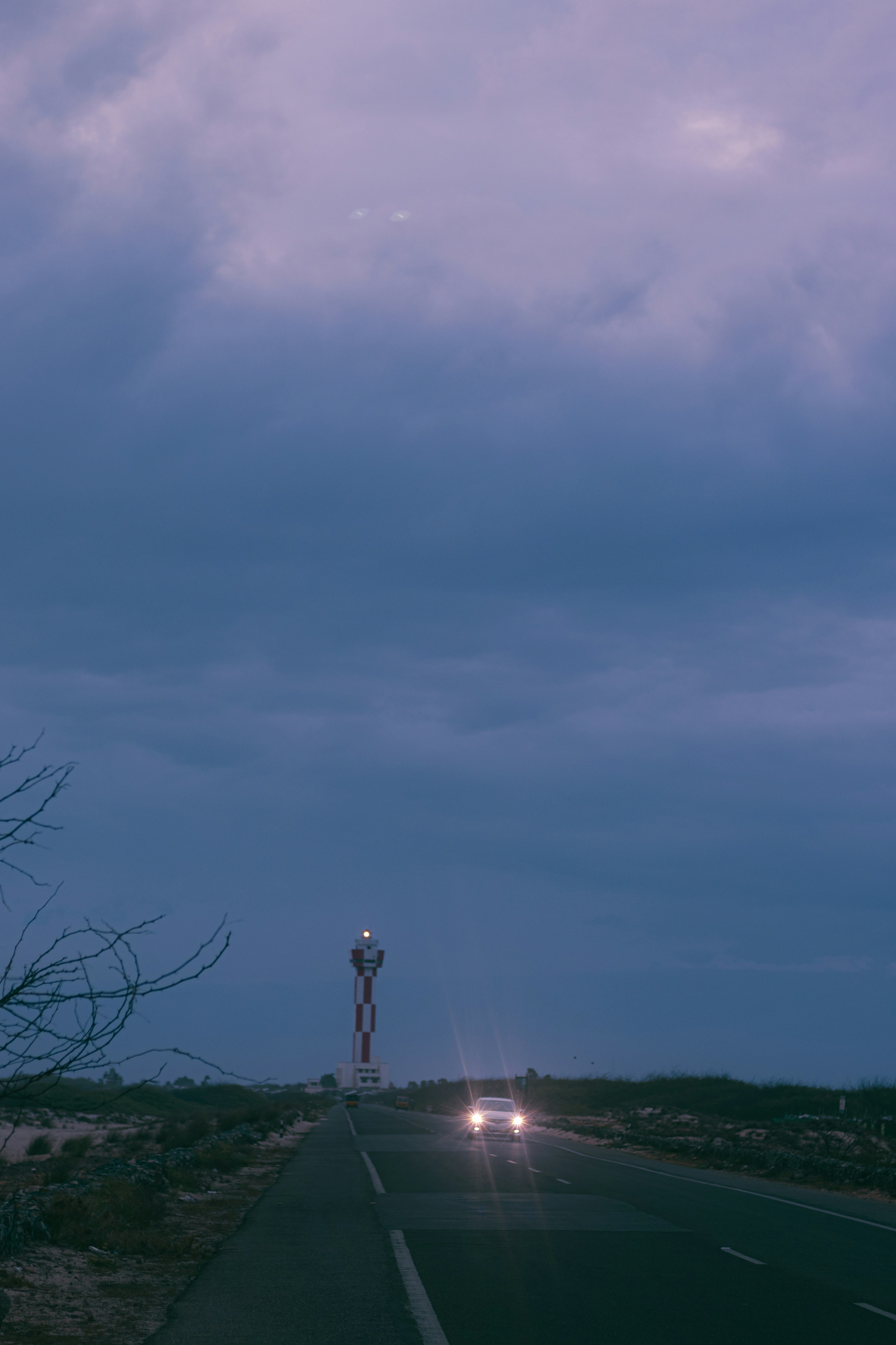 A solitary car approaches a distant lighthouse under a moody, overcast sky. The scene captures the essence of navigation and solitude.