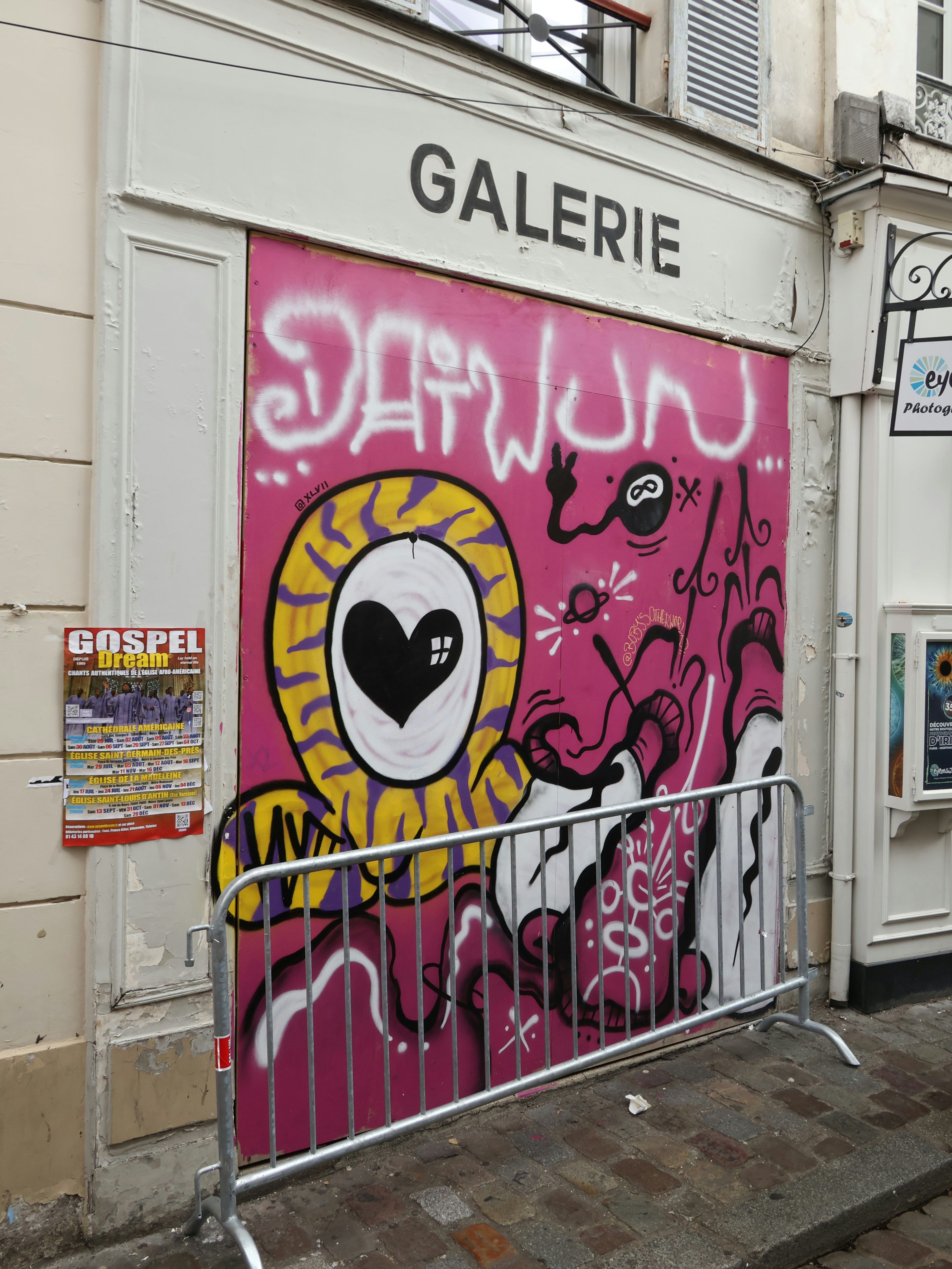 Pink storefront mural at Galerie with bold eye motif behind barrier
