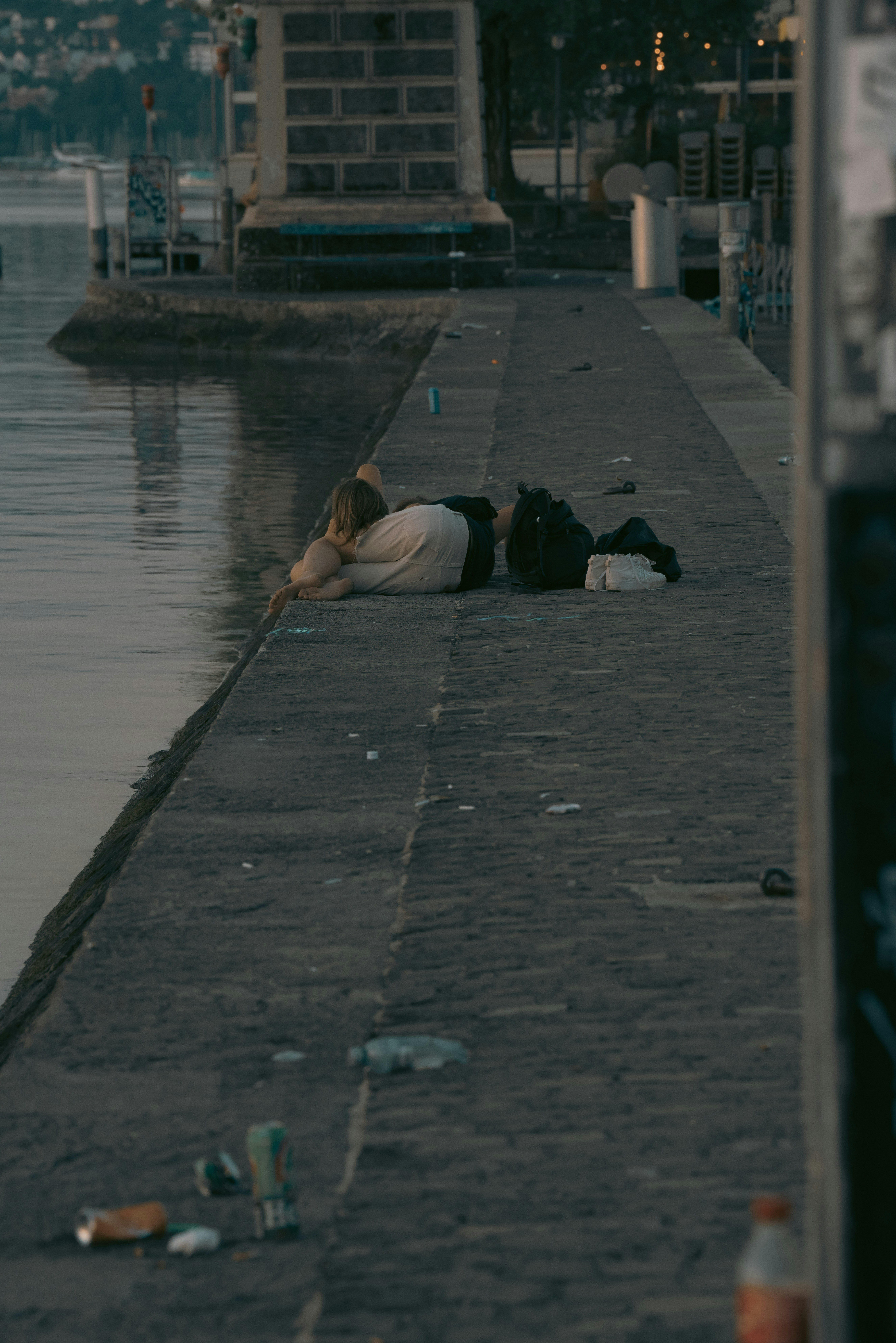 Person sleeping on a waterfront walkway with trash.