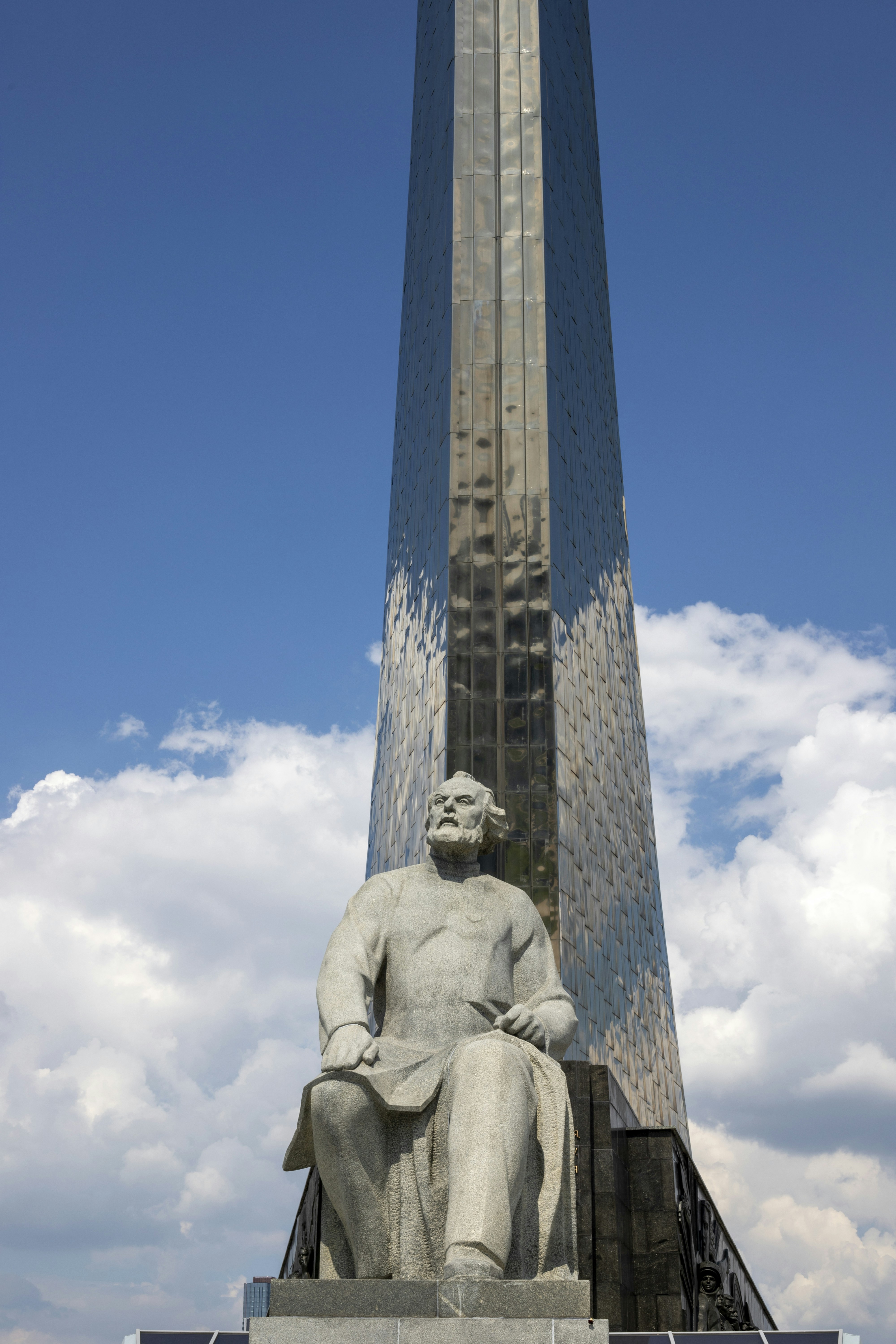 Statue in front of a tall, reflective monument.