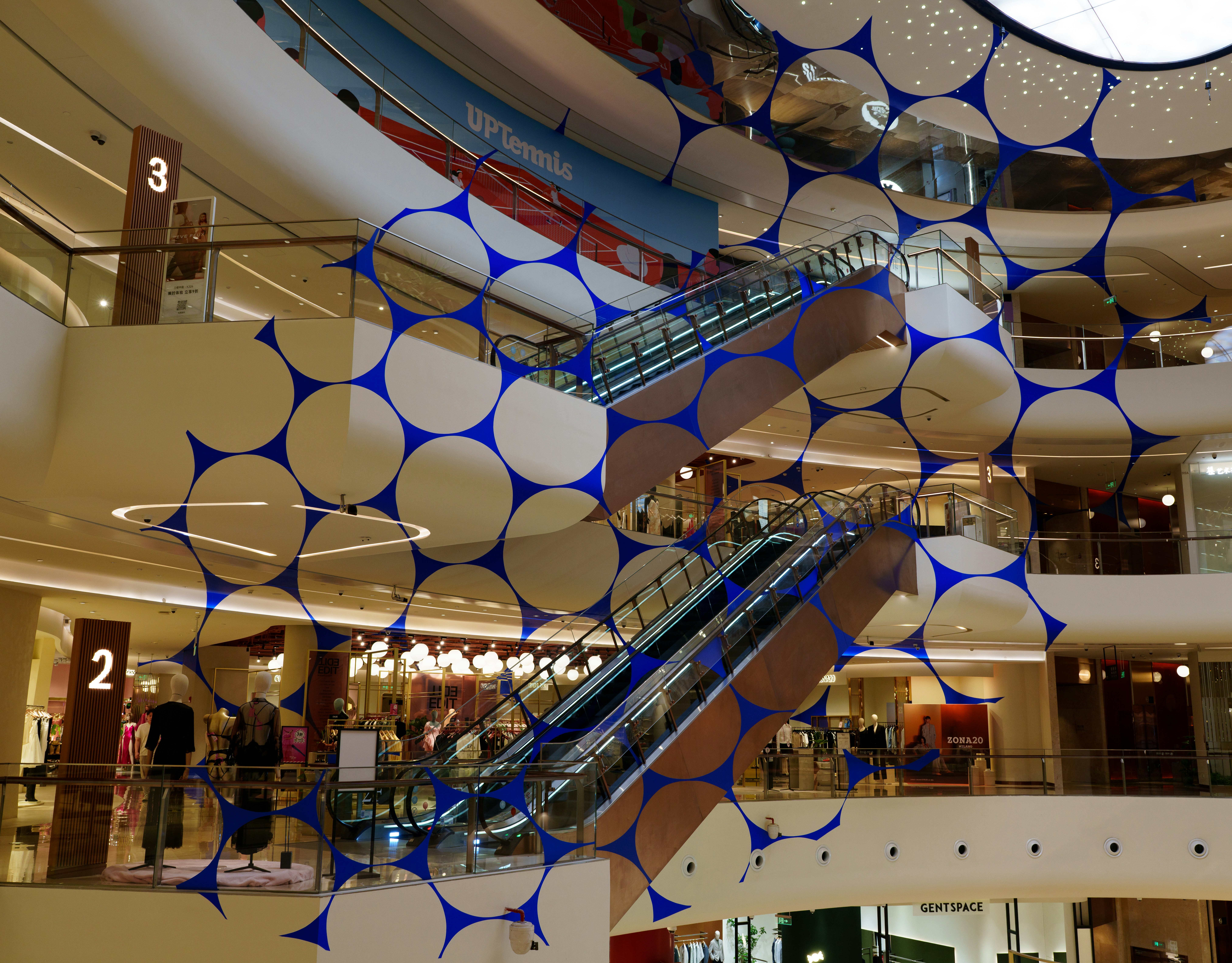 Modern shopping mall interior with escalators and people.