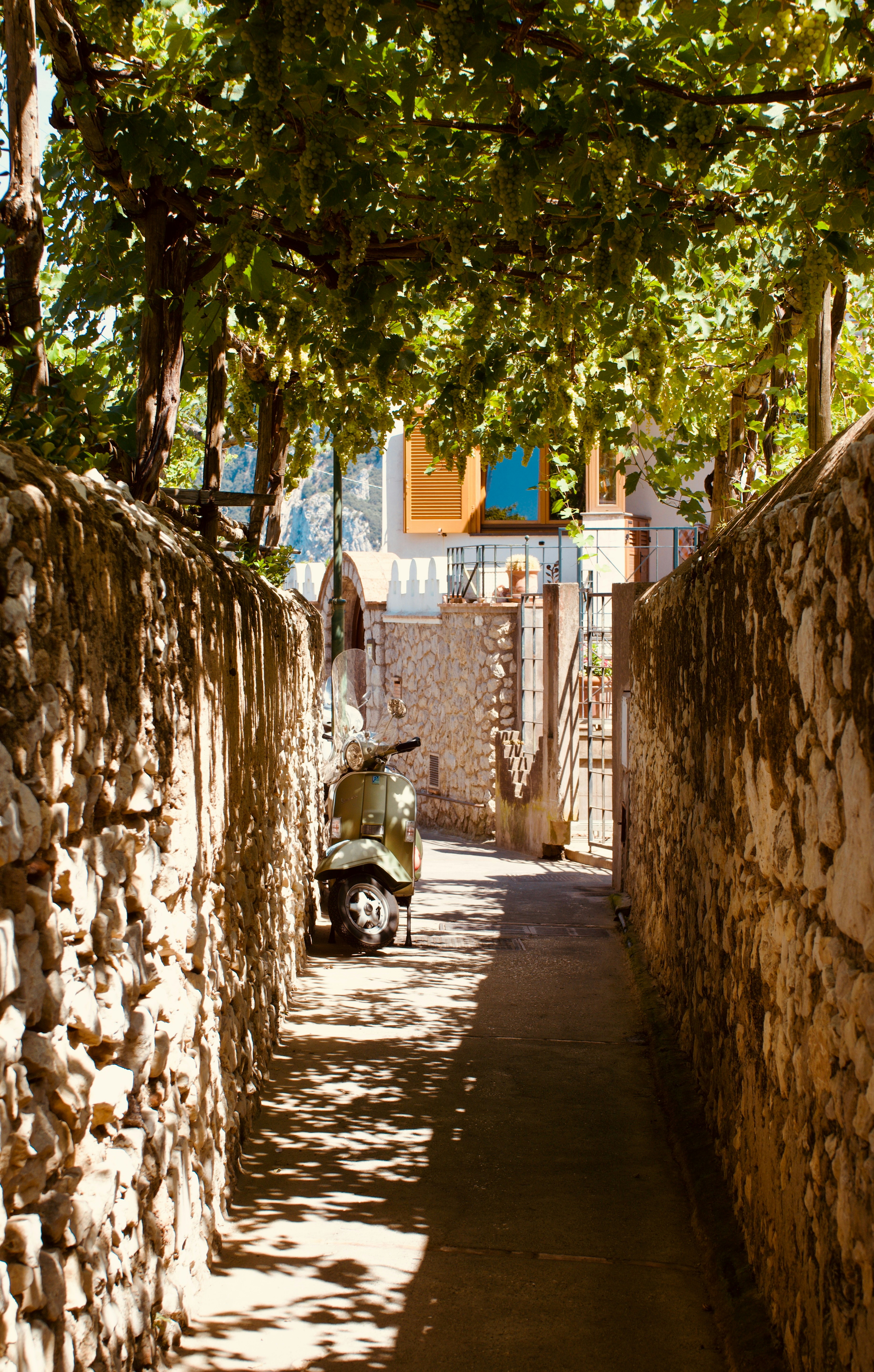 Scooter in Isle Of Capri, Italy. | Narrow alleyway with stone walls and a scooter.