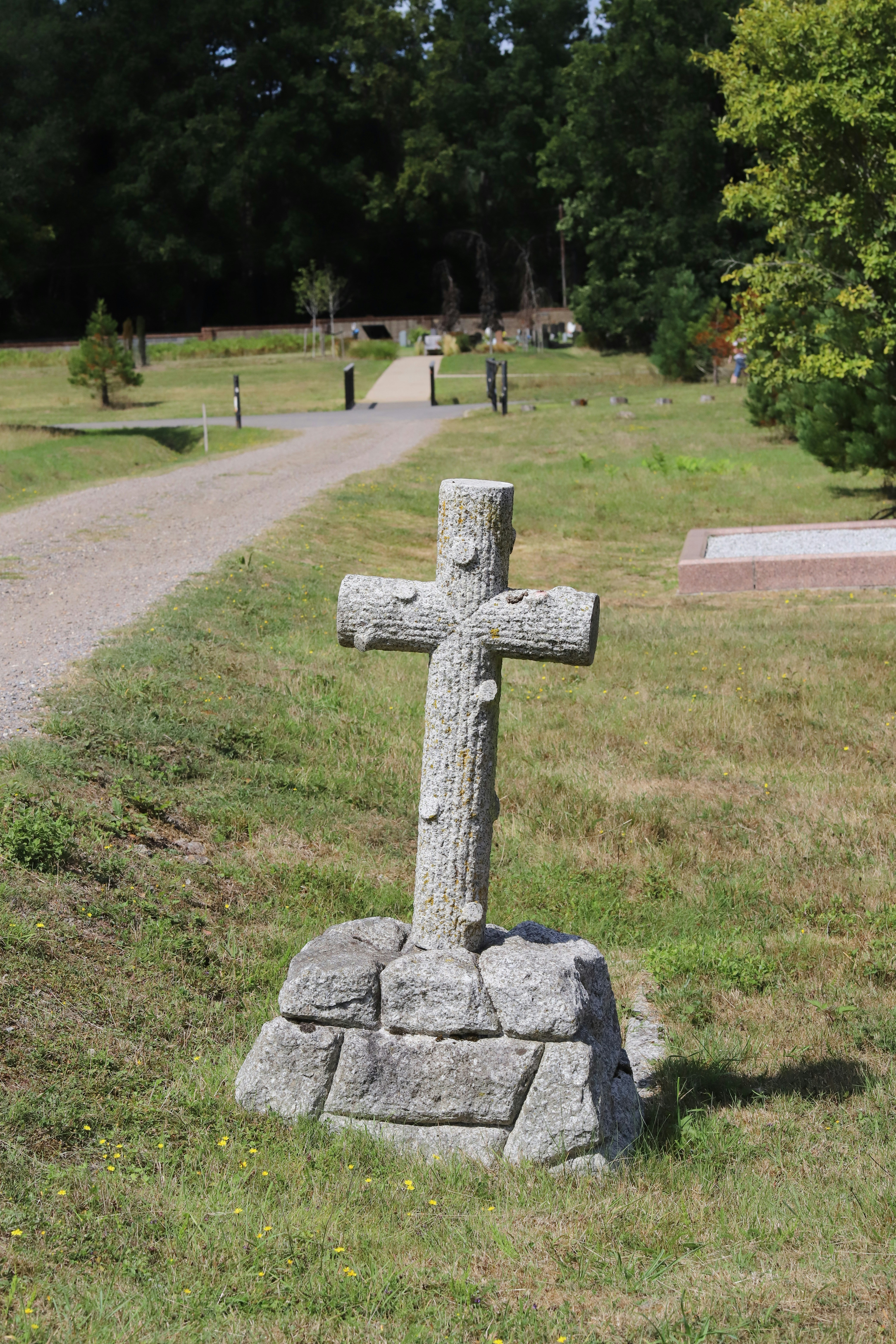 Stone cross in a grassy cemetery with a path.