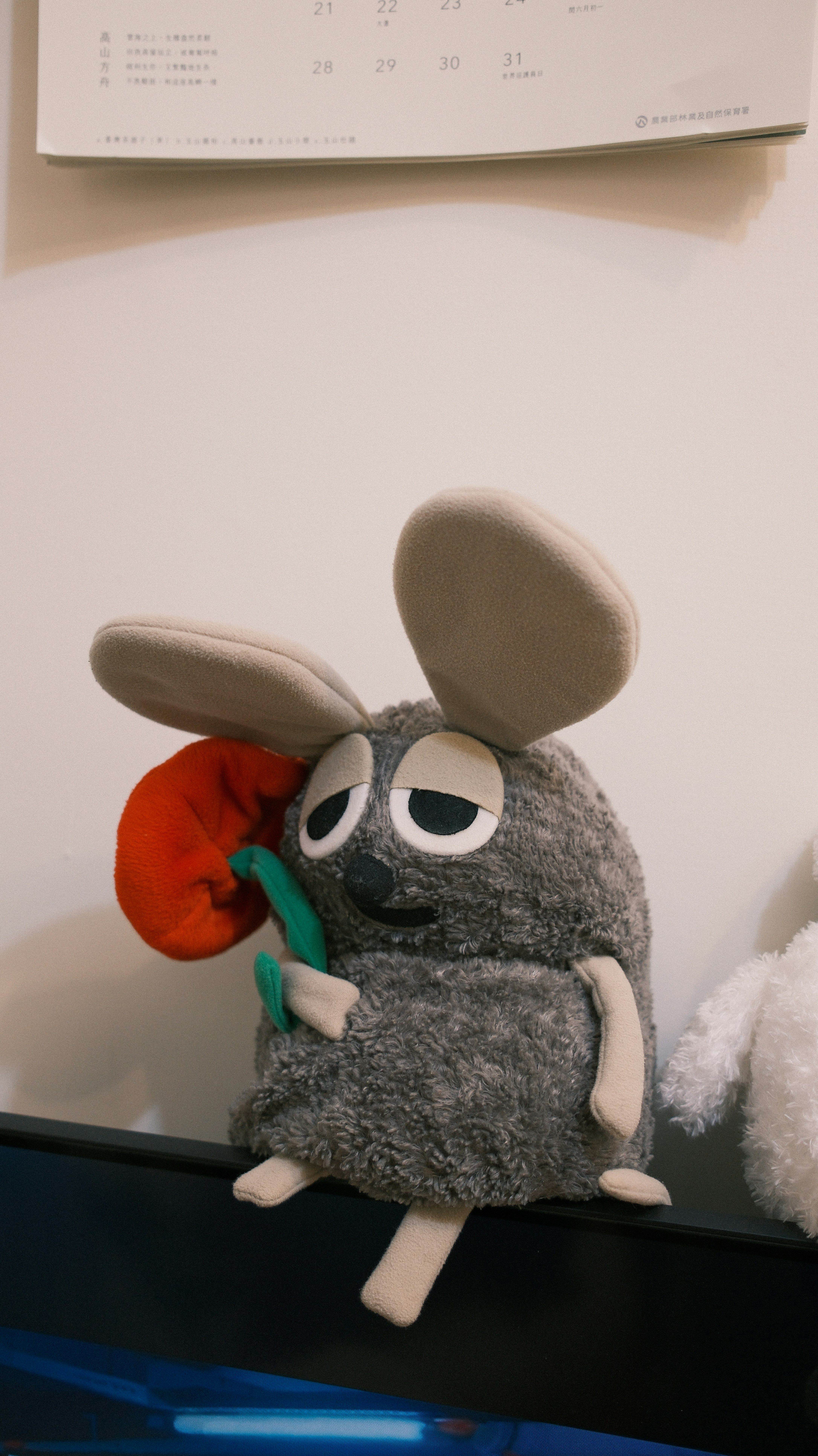 A fluffy gray toy mouse holds a red flower.