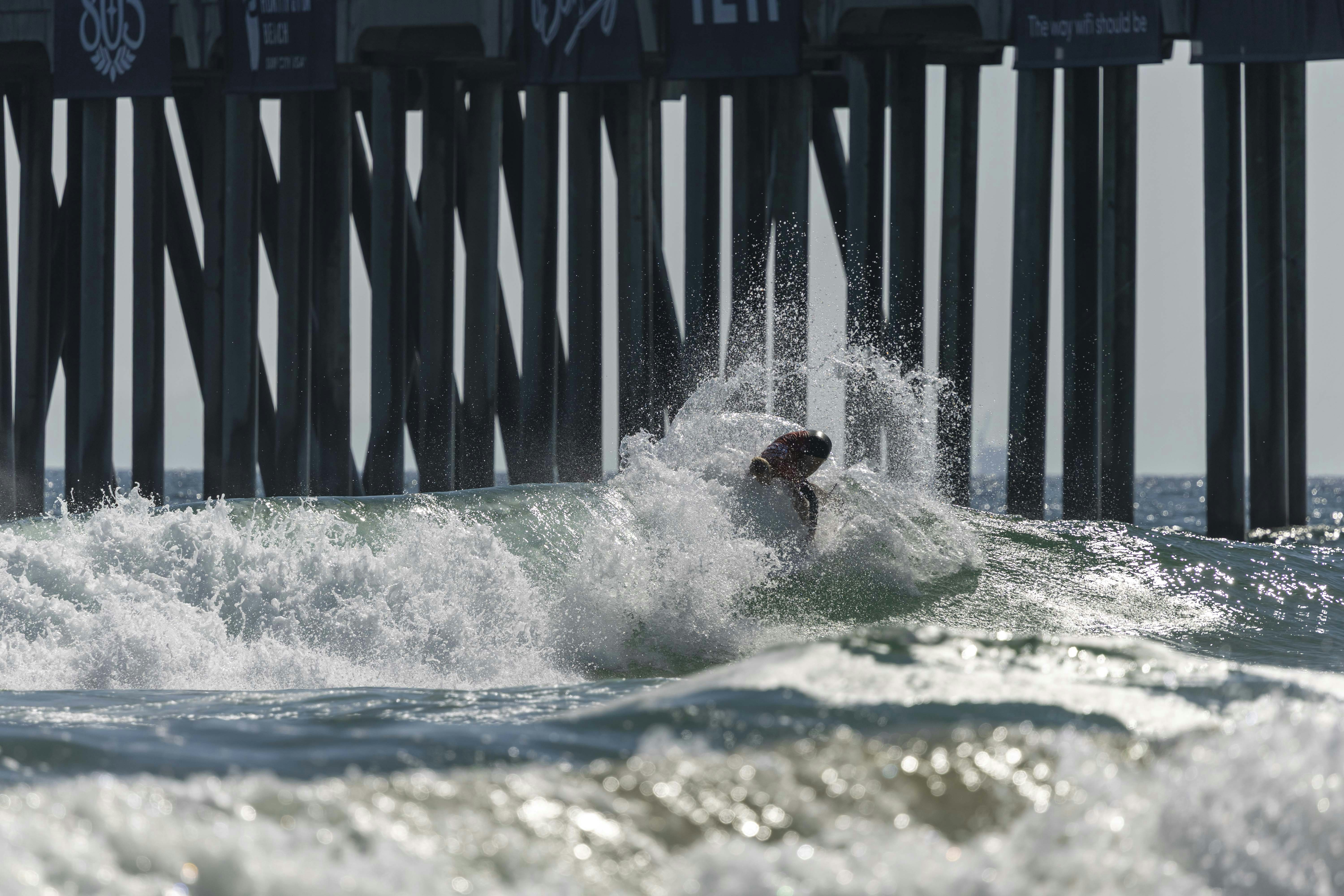 Surfer riding a wave under a pier